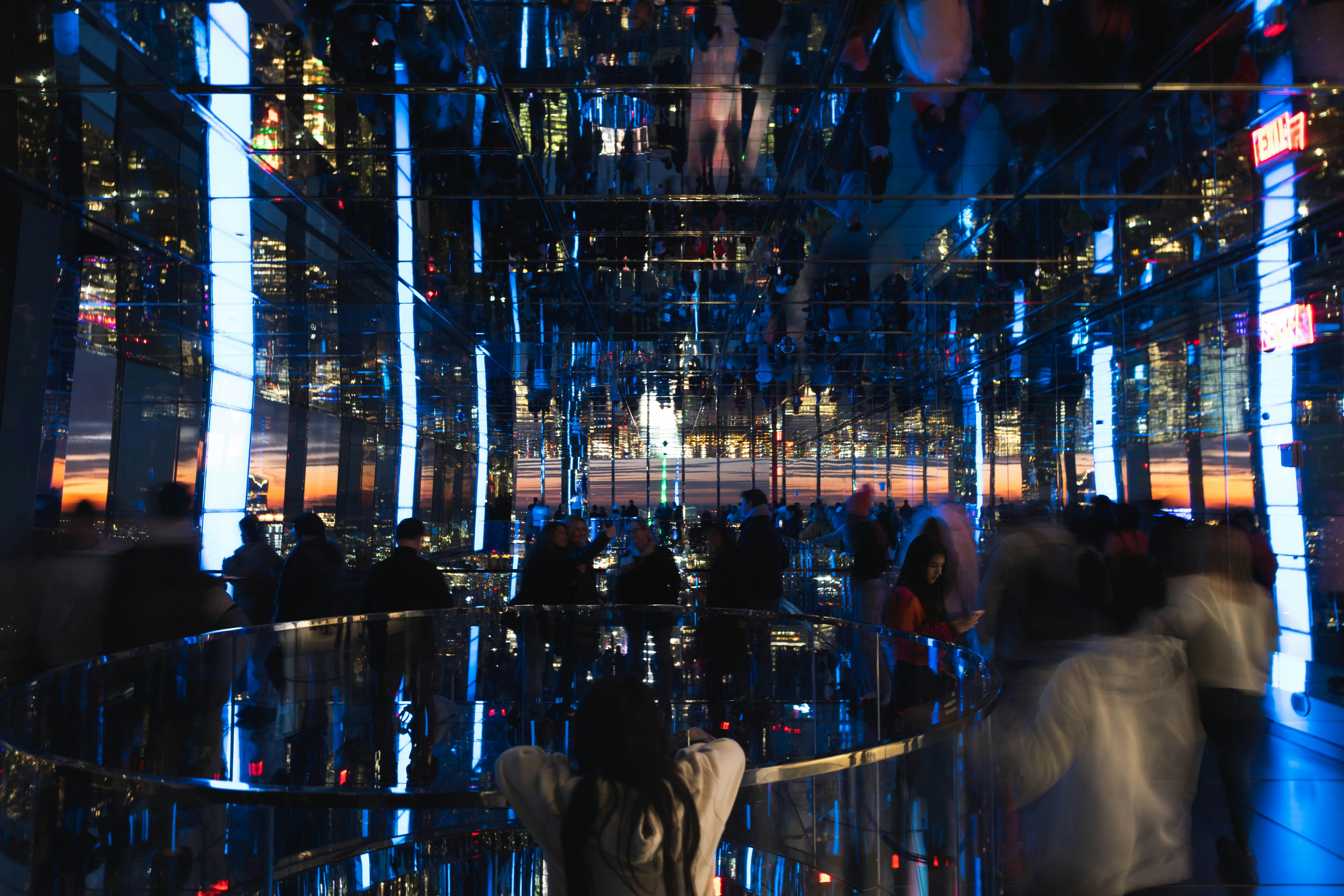 Crowd of visitors immersed in a mirrored space, capturing the vibrant cityscape at dusk.