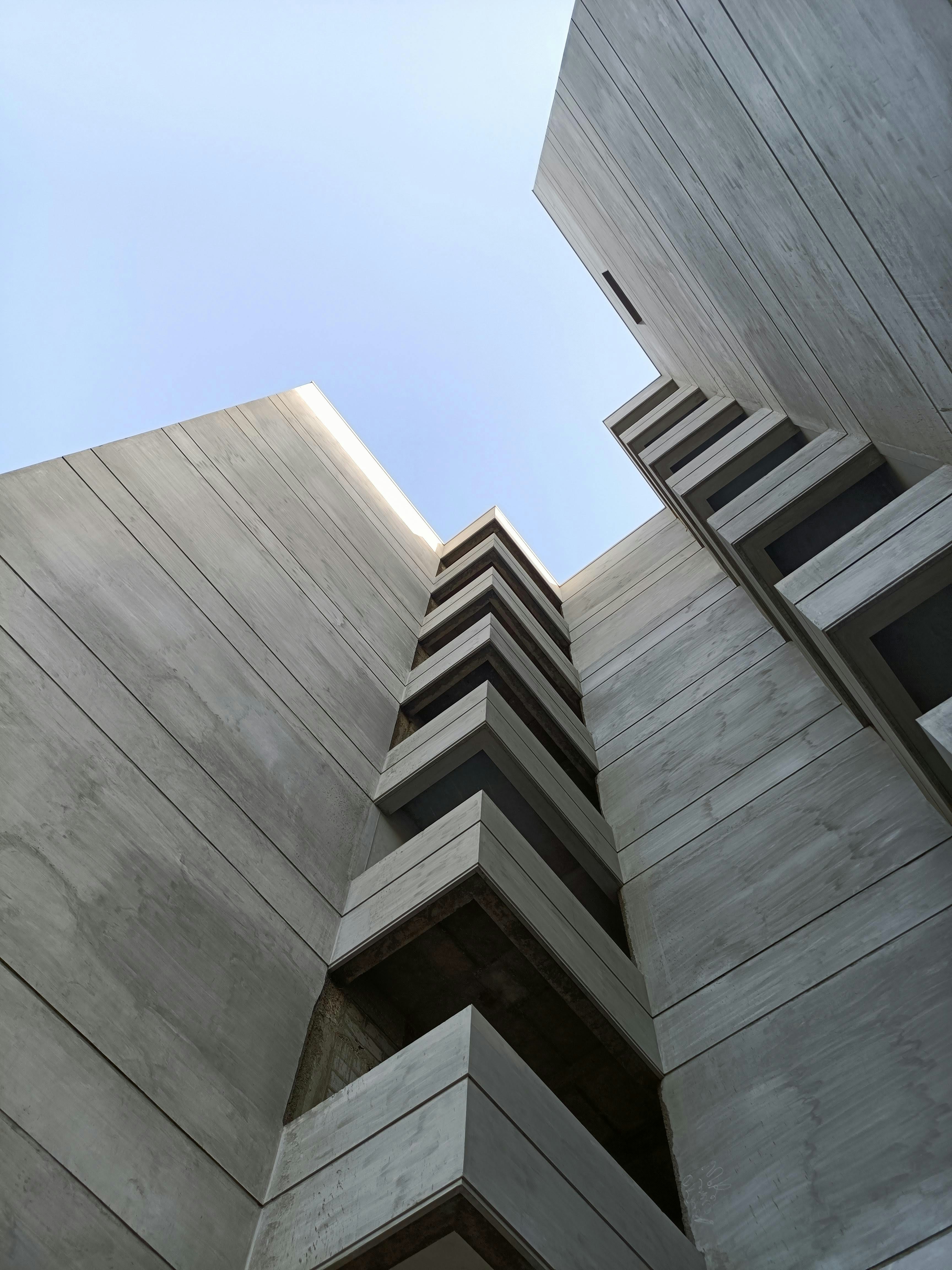 Abstract architectural view looking up at concrete structures converging towards a clear blue sky.