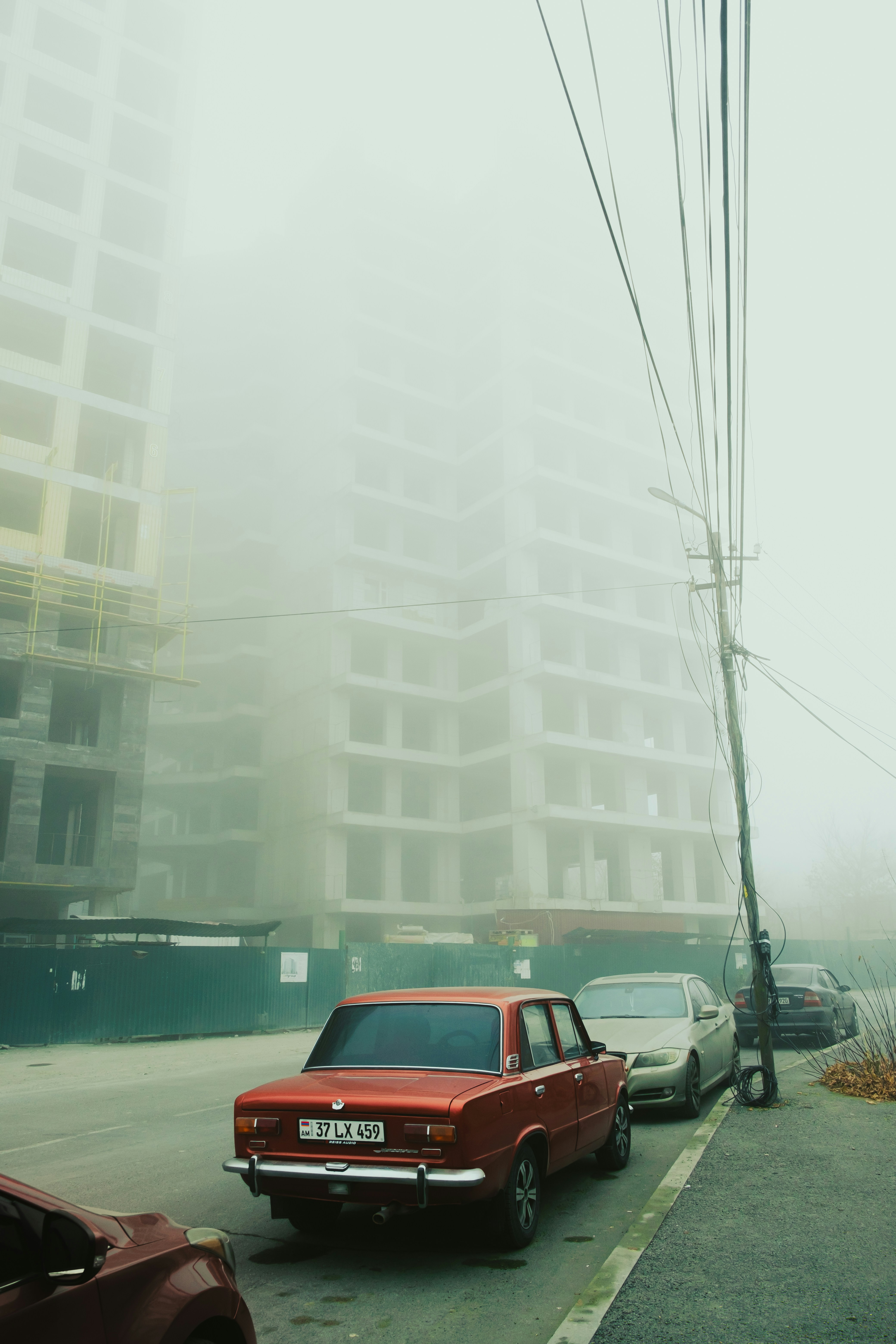 Red vintage car anchors a foggy urban crawl under rising concrete skeletons