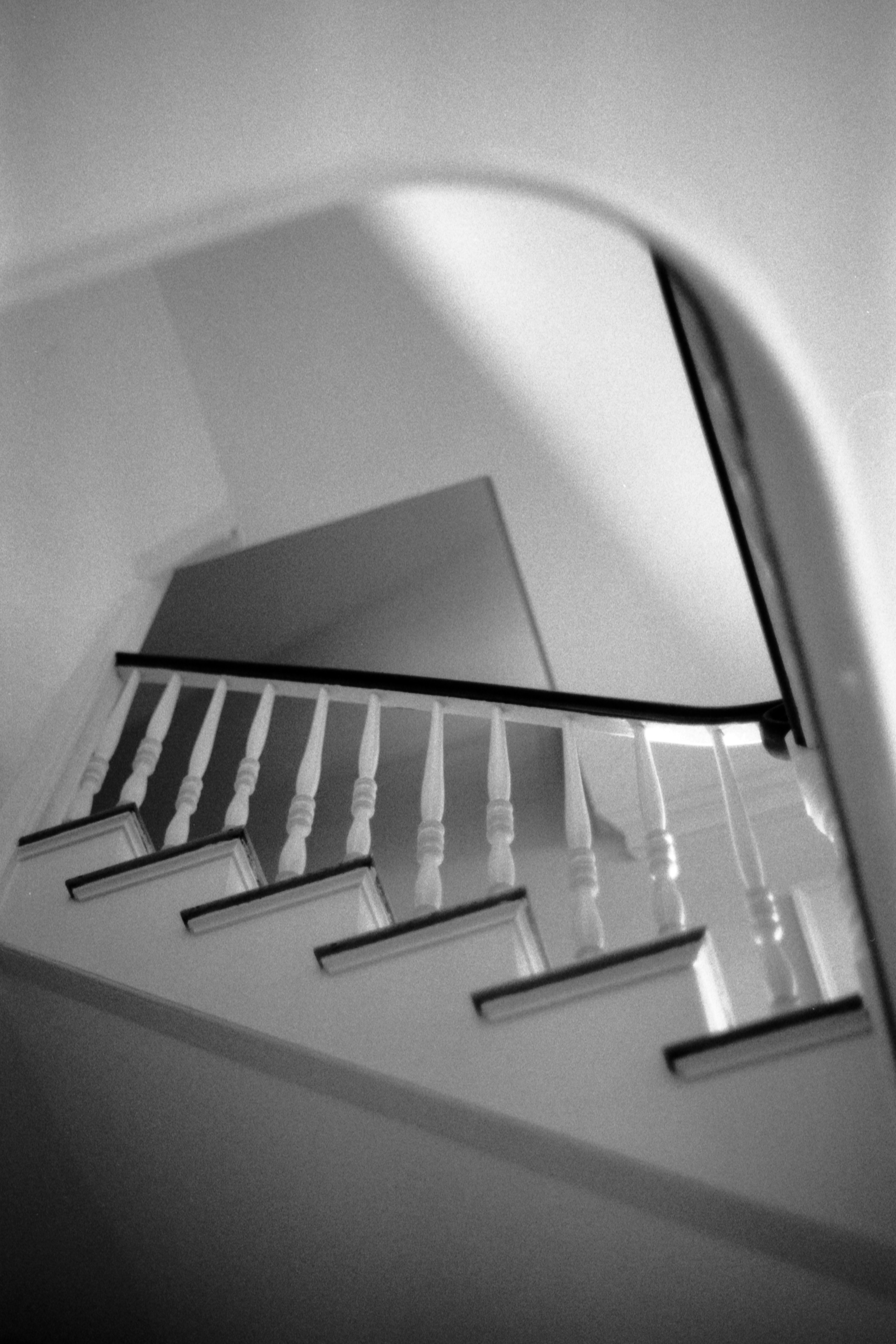 Monochrome photograph of a wooden staircase with turned balusters, viewed through a curved doorway that frames the ascent.