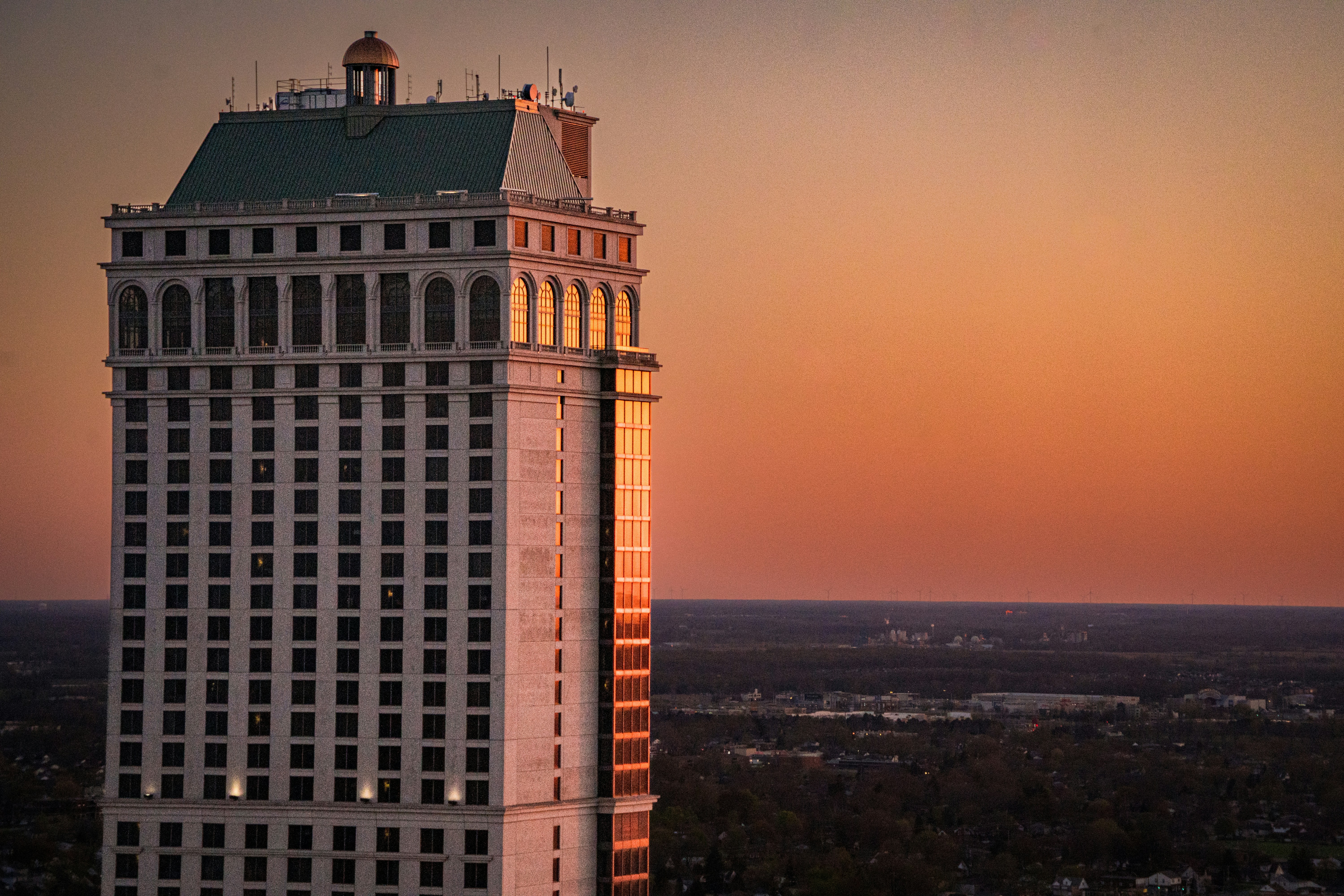 Tall building with arched windows reflecting sunset hues against a vast cityscape.