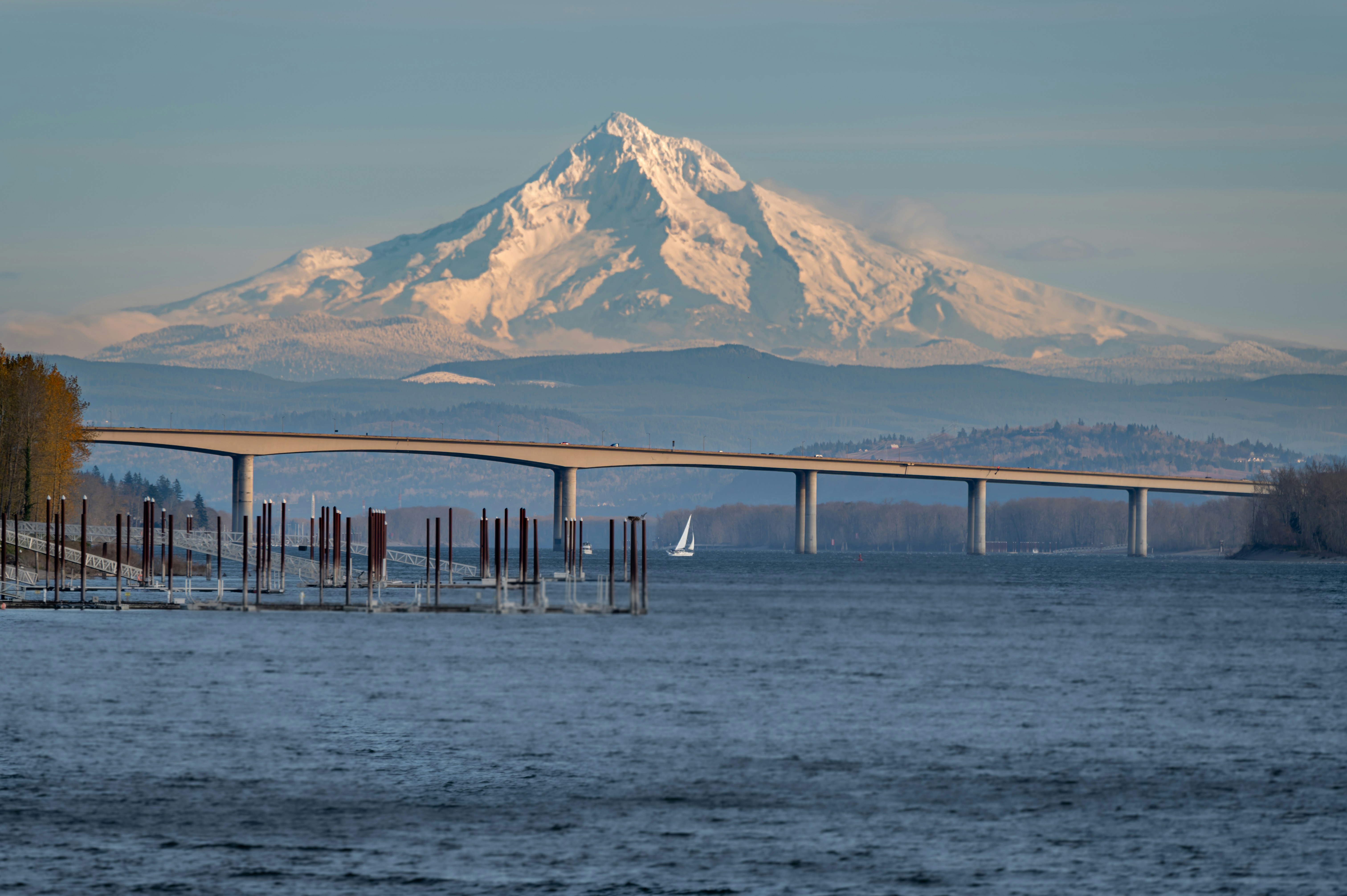 Mount Hood bathed in sunset light, with a bridge and sailboat in the foreground.