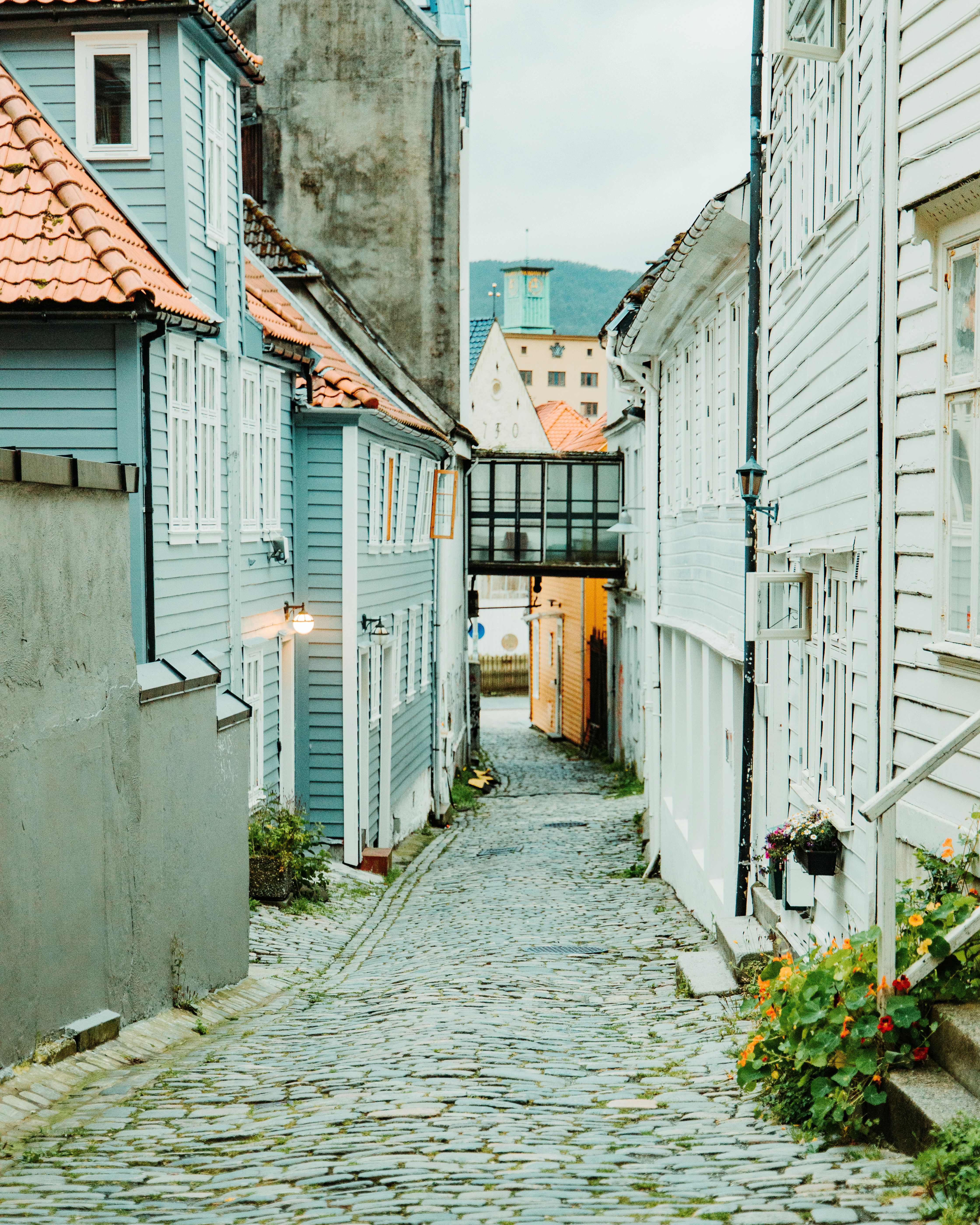 Charming cobblestone alleyway flanked by traditional wooden houses, leading to a modern overpass, showcasing a blend of history and contemporary architecture.