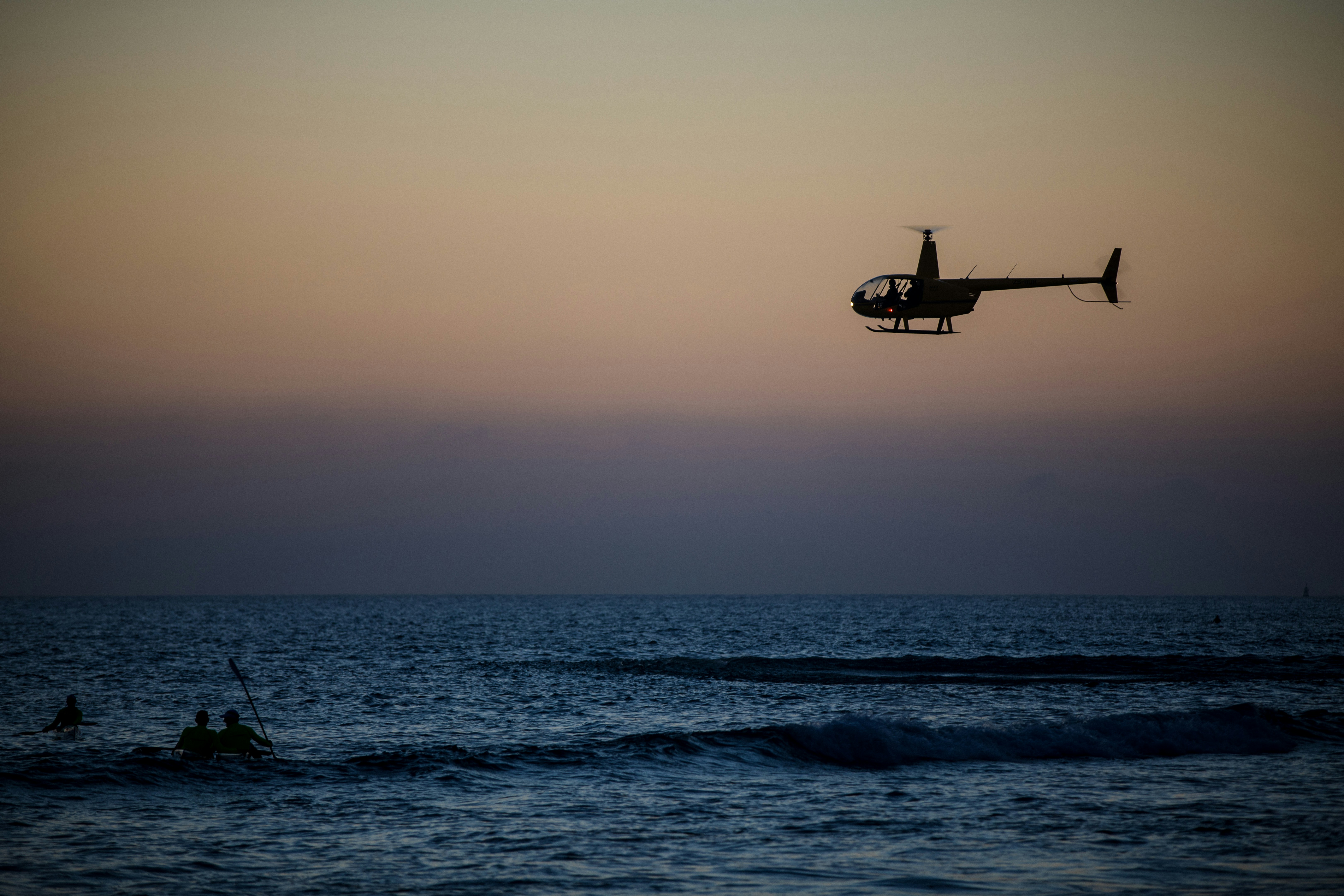 Silhouette Above the Horizon: Helicopter Over Quiet Seas at Dusk