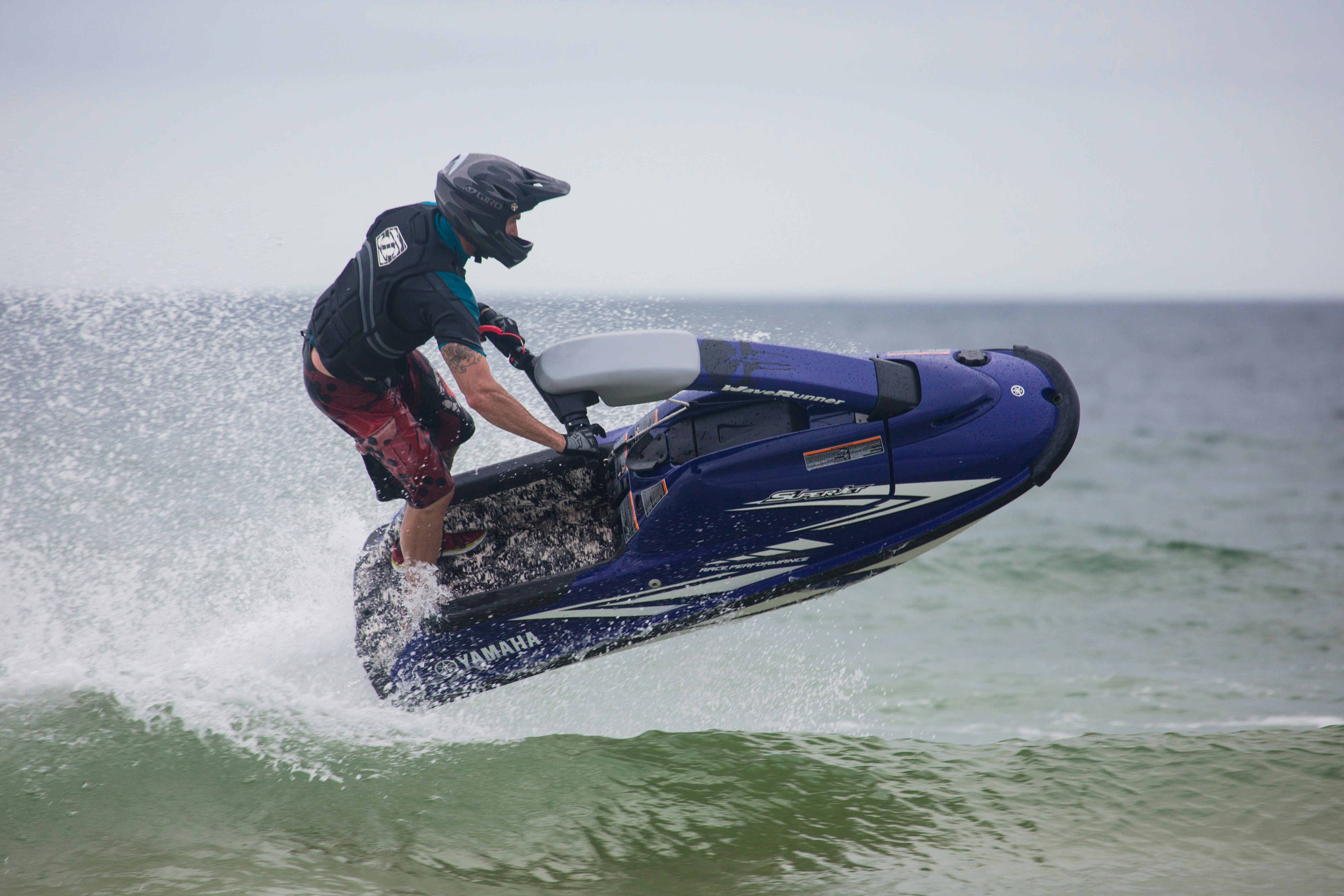 A rider performs a daring jump on a jet ski, sending up a spray of water against the backdrop of a calm sea. The action captures the excitement of water sports.