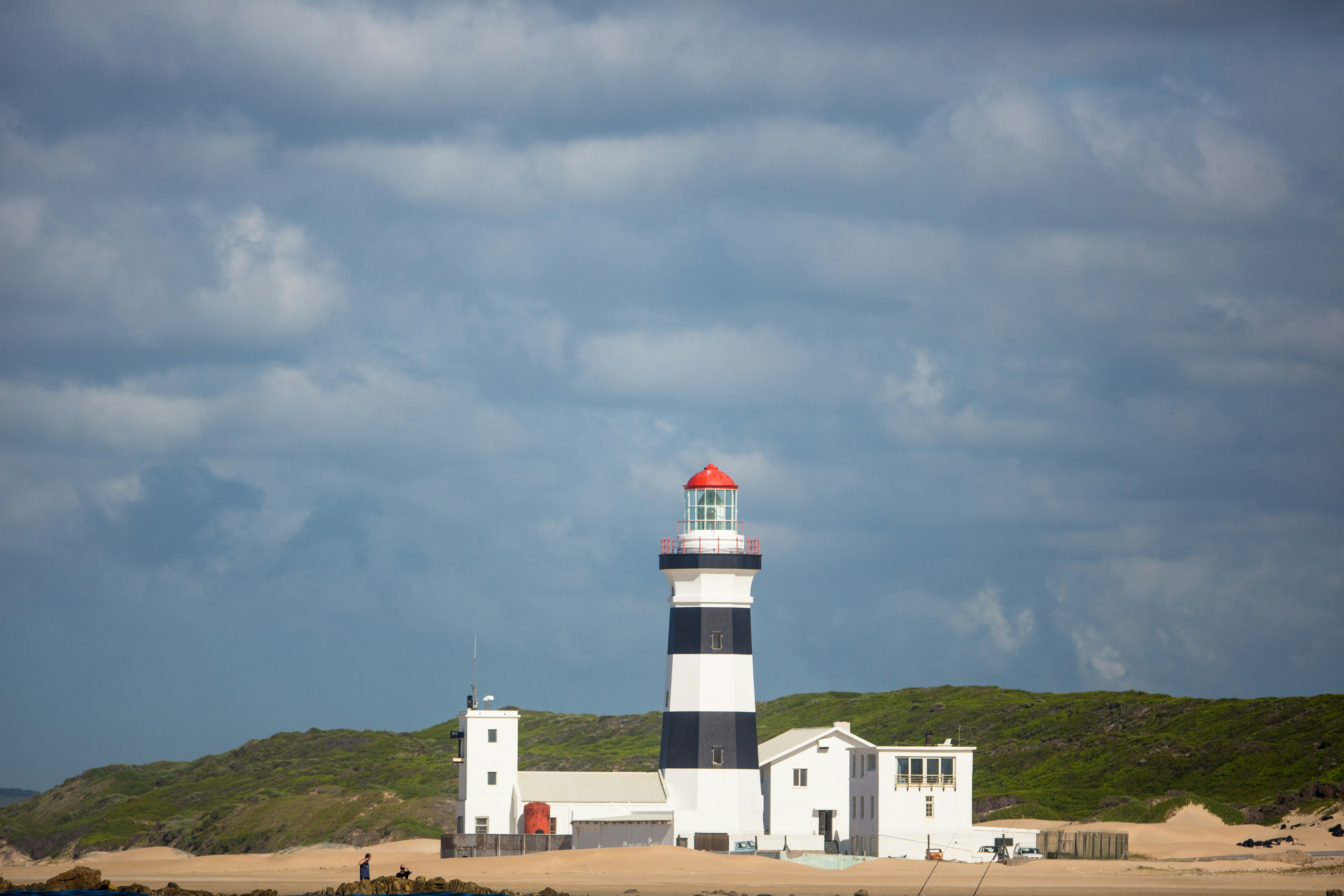 A white and black and red lighthouse on a beach photo – Free Beacon ...