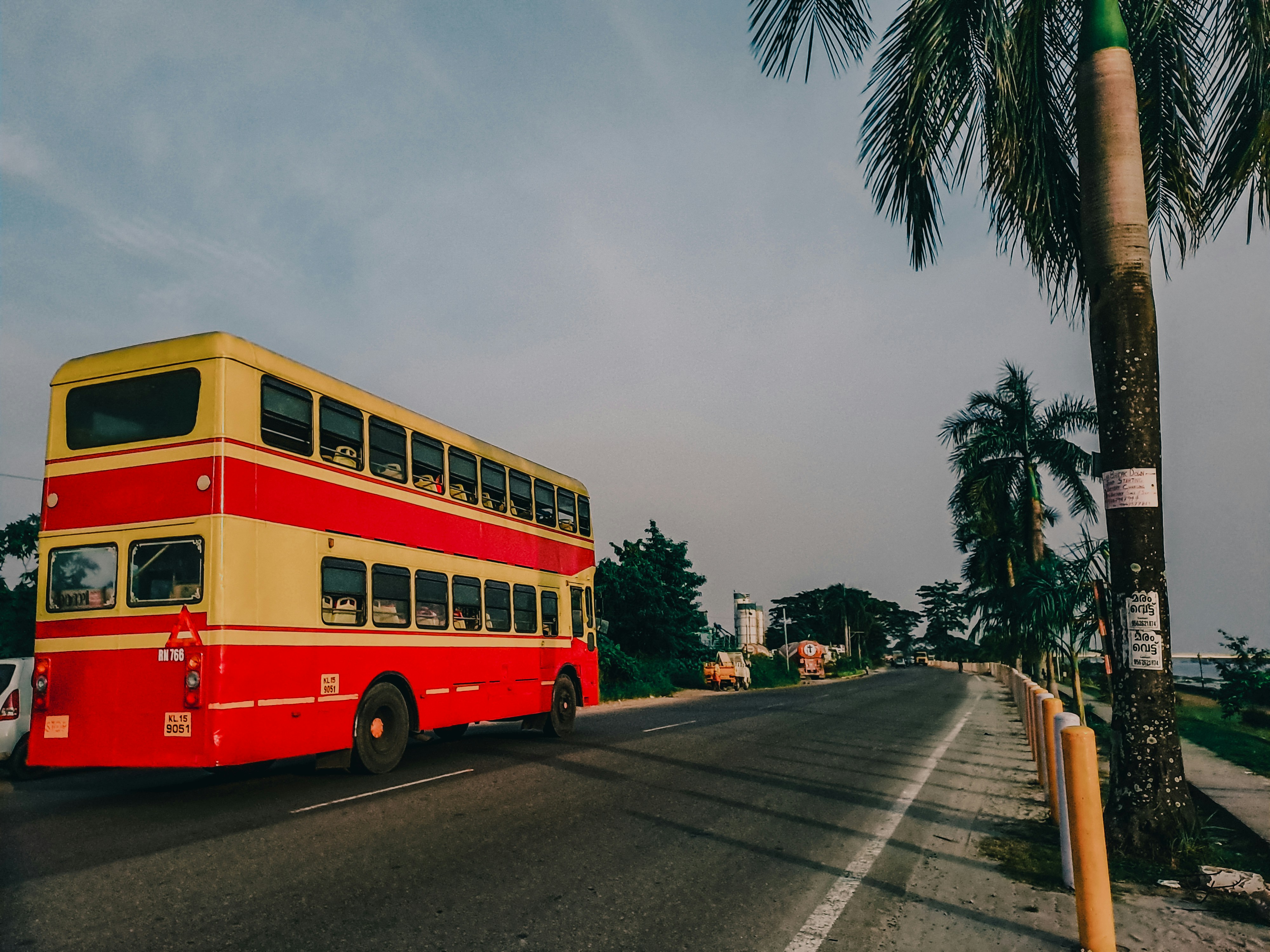 A vibrant red and yellow double-decker bus navigates a quiet road lined with palm trees, evoking a sense of nostalgia and urban exploration.
