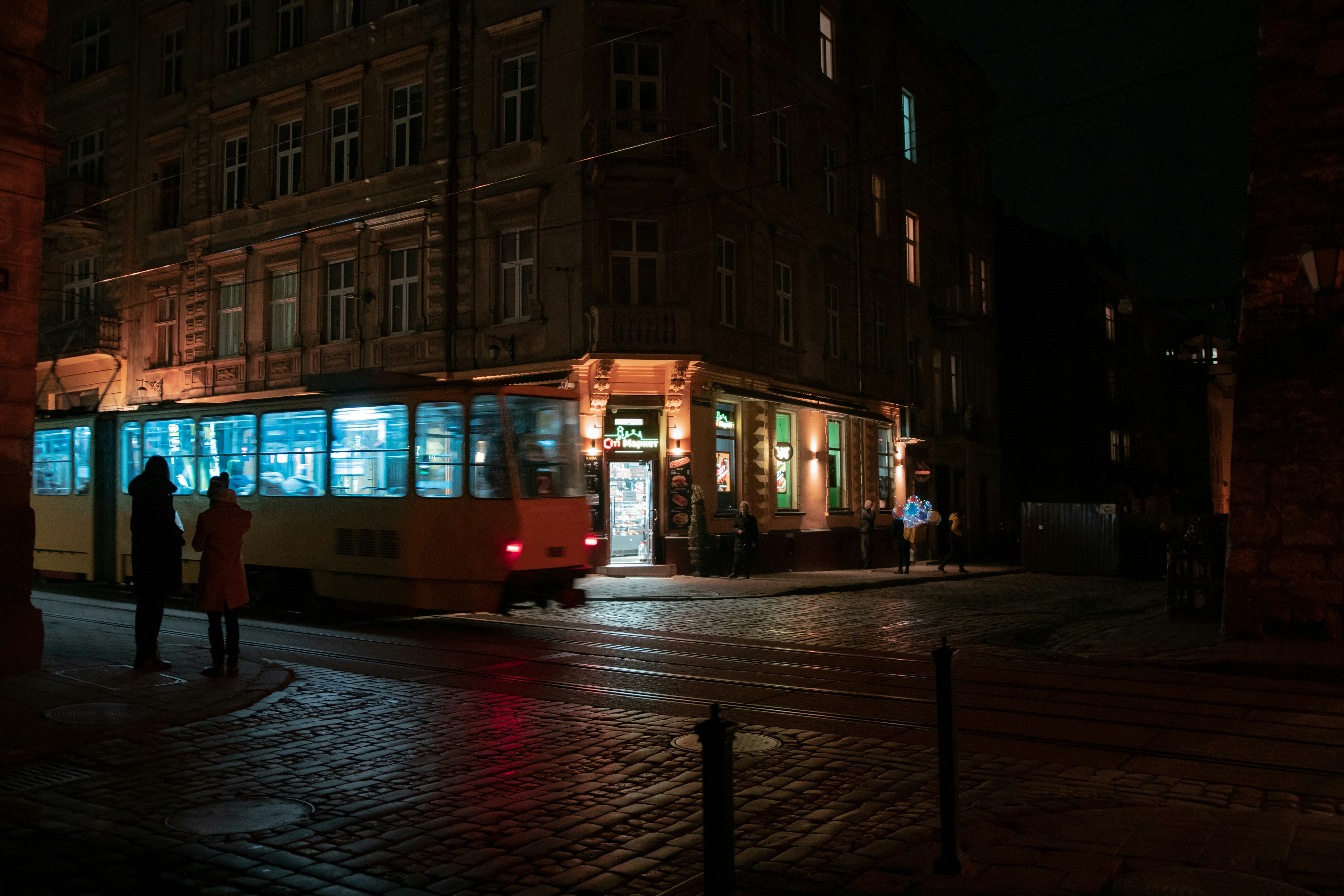 Blue-tinged tram gliding past a rain-kissed city corner after dark