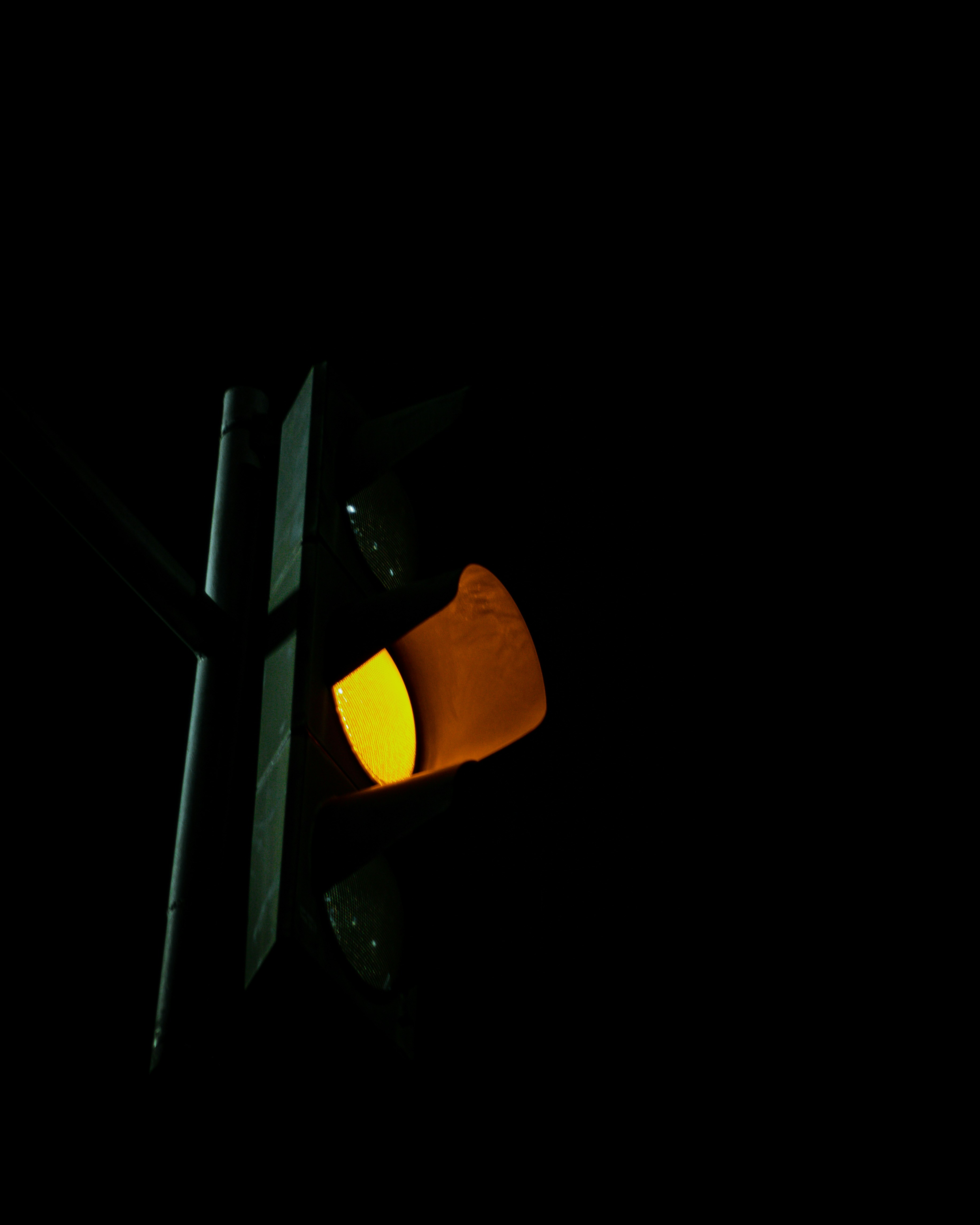 Orange traffic light glowing against a pitch-black backdrop, signaling caution and alertness.