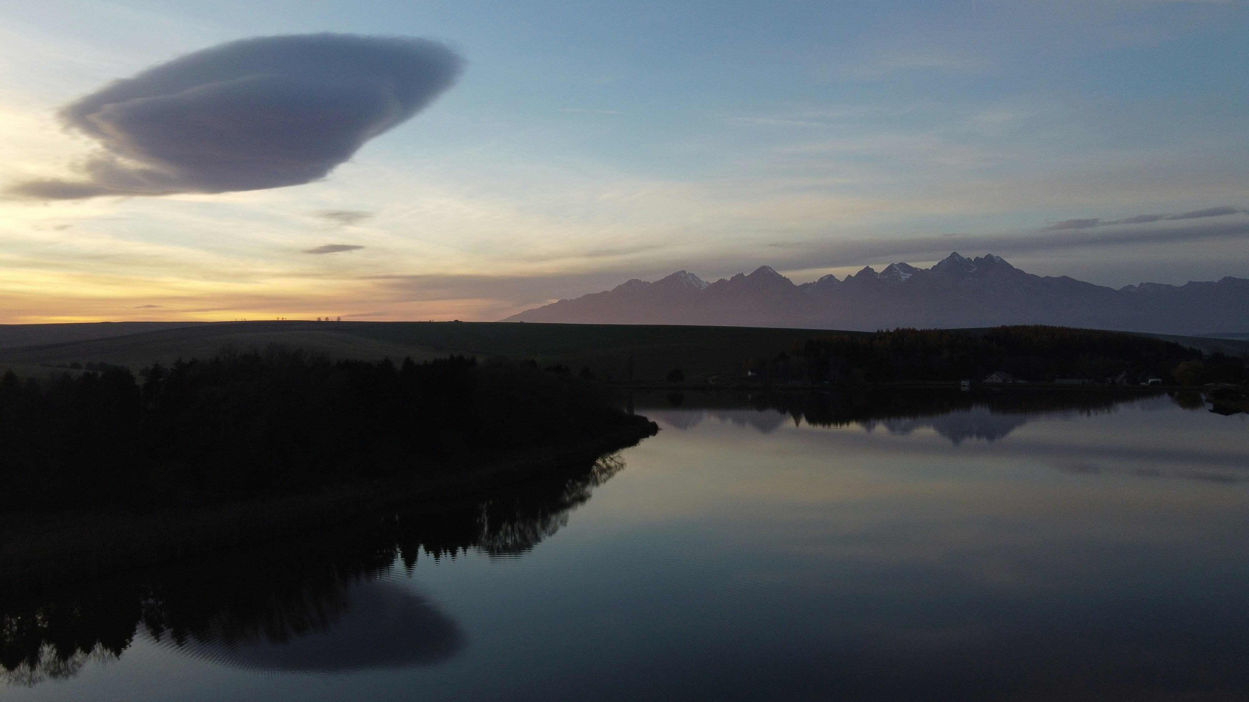 A serene landscape featuring a reflective lake under a vibrant twilight sky, with distant mountains silhouetted against the horizon.