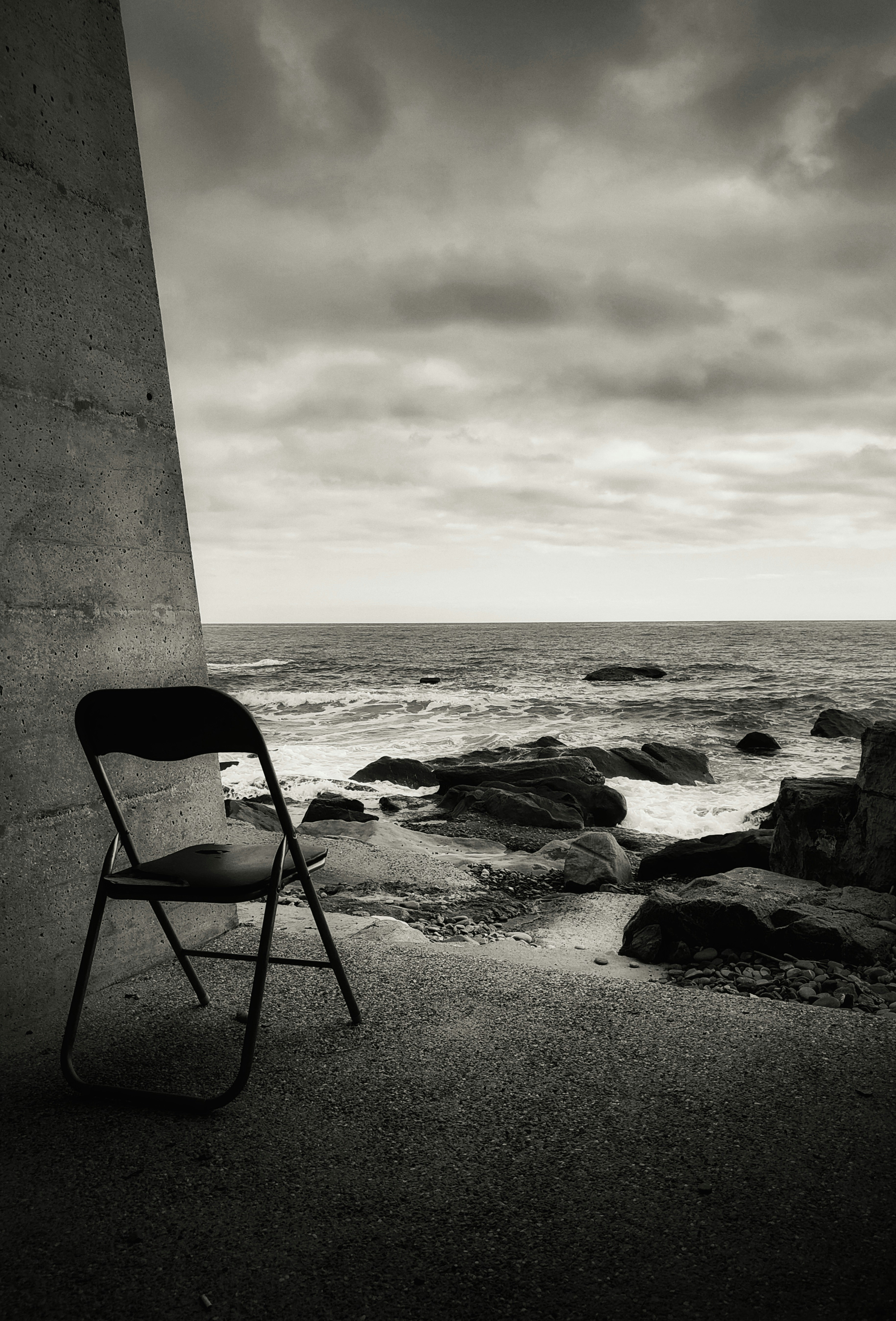 Grayscale Solitude: A Folding Chair at the Edge of the Sea