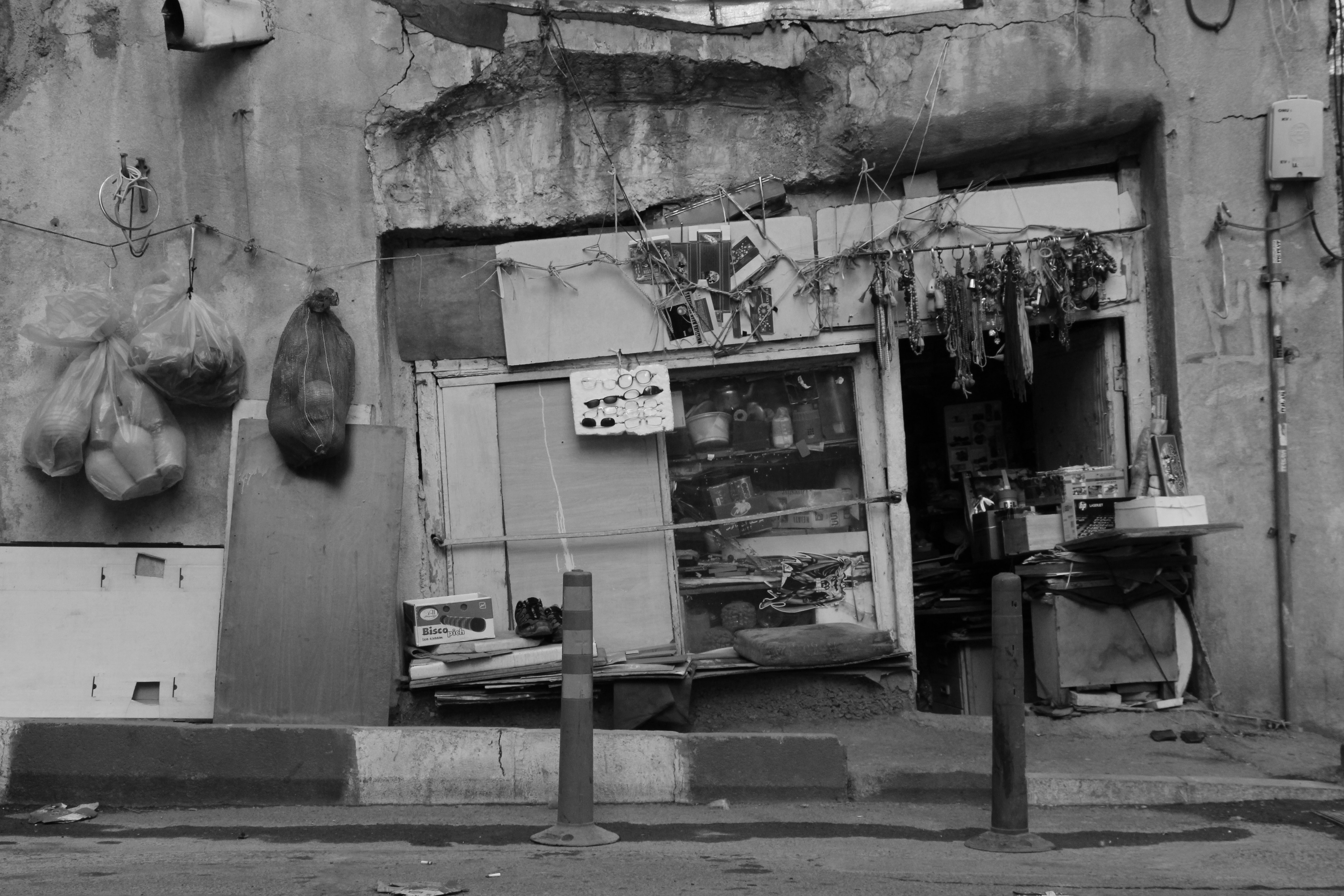 A weathered storefront filled with various items, showcasing the essence of local commerce. Plastic bags hang beside the entrance, hinting at the shop's daily activities.