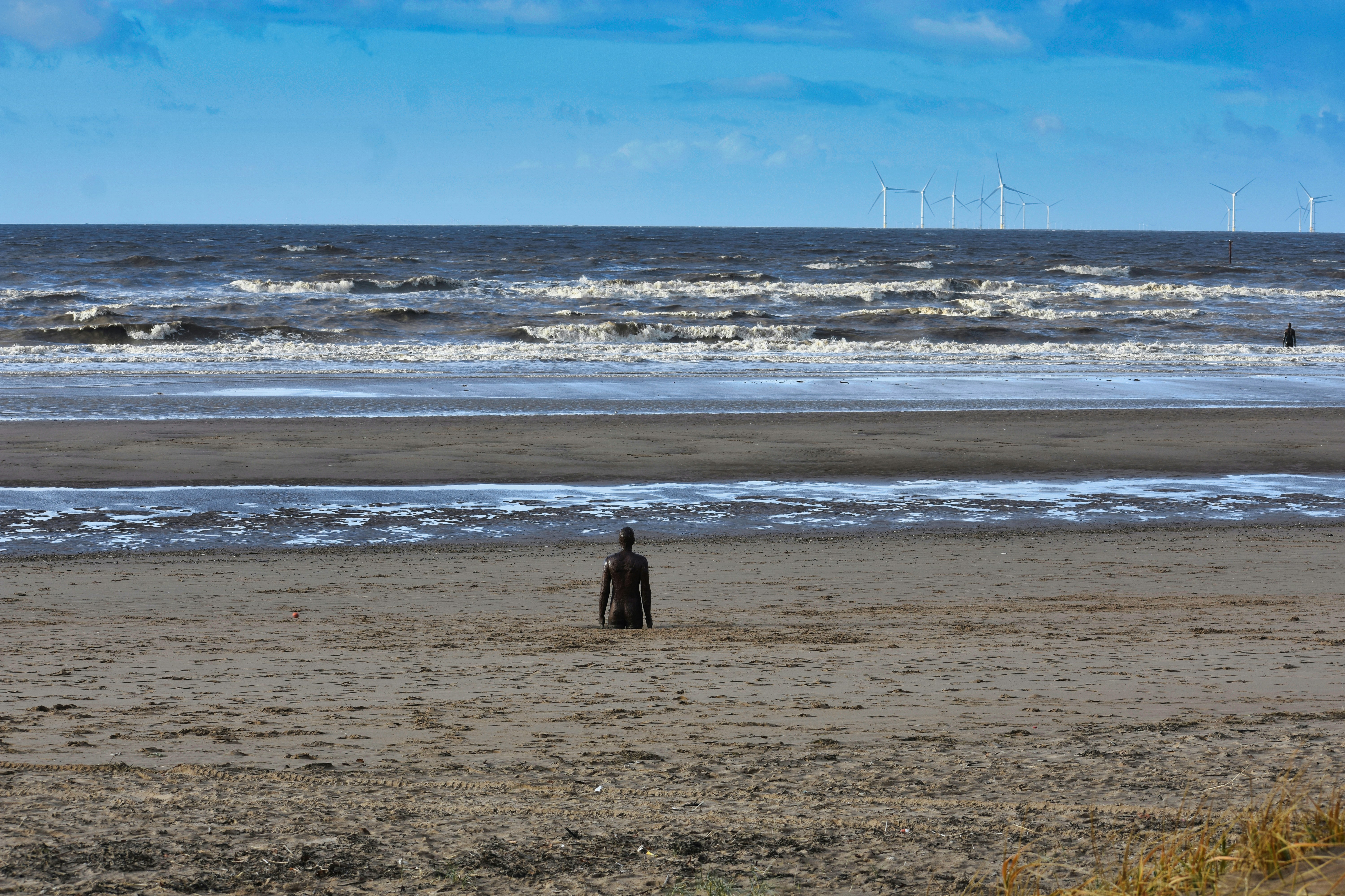 Lone Figure on Quiet Shore as Wind Turbines Crown the Distant Horizon