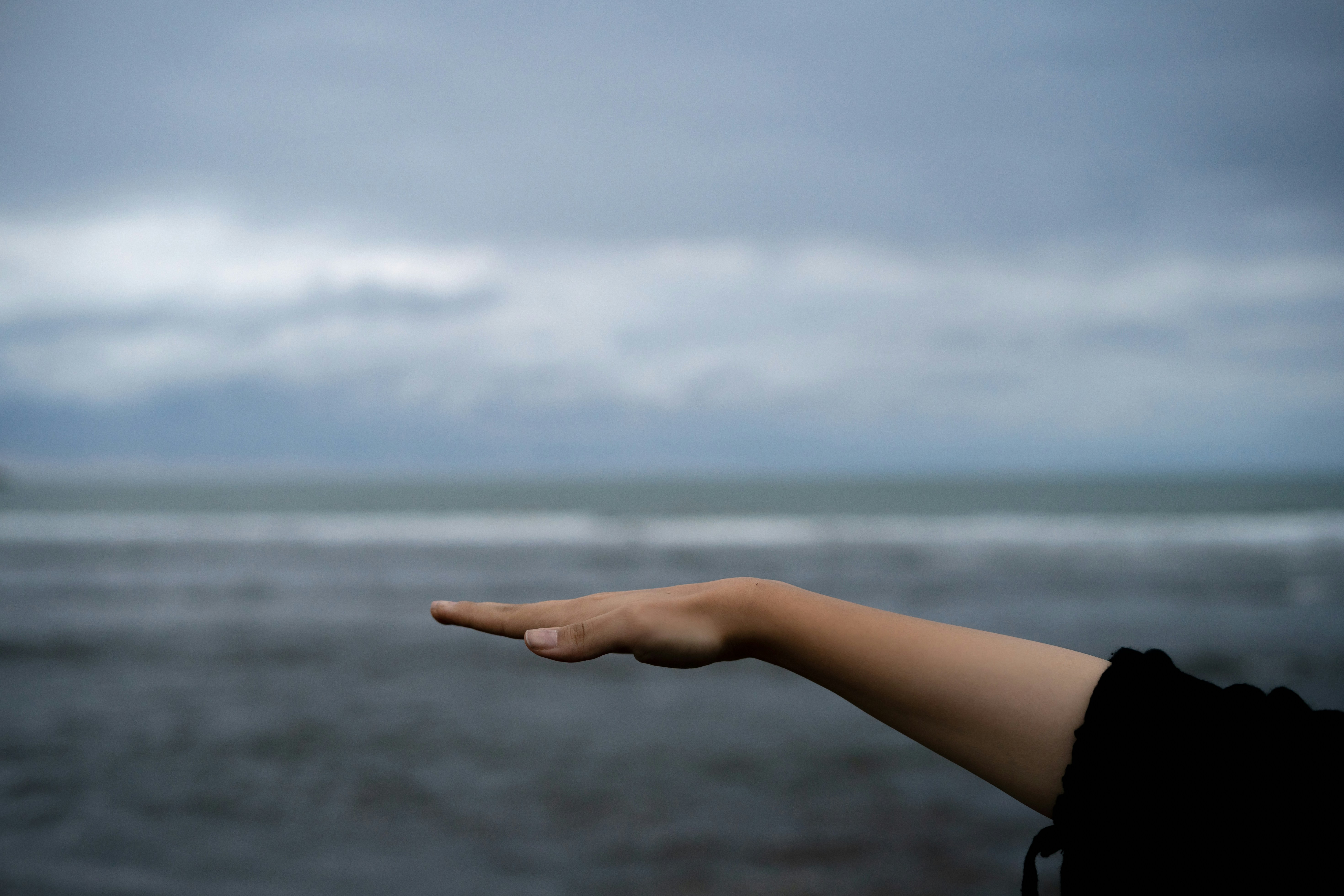 Outstretched Hand Framing a Distant Sea Under Muted Skies