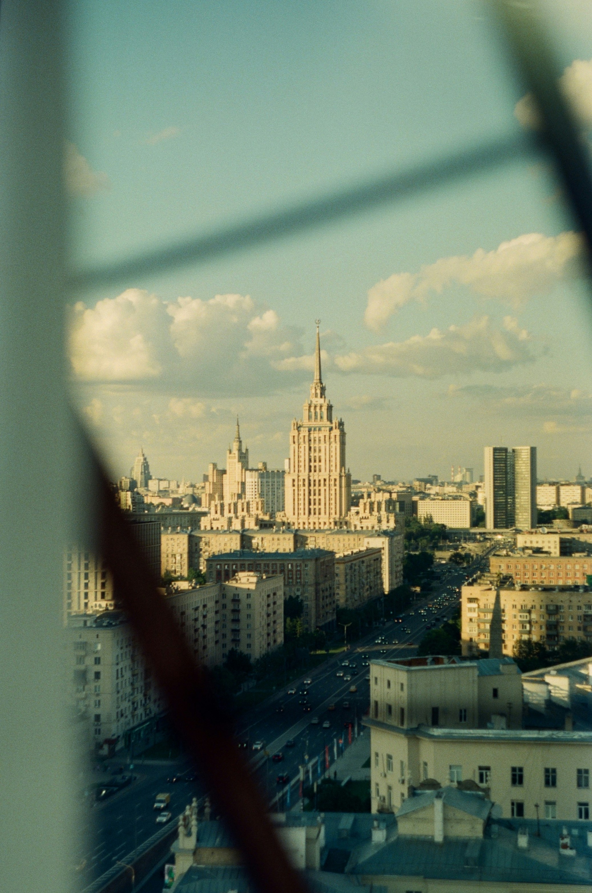 View of a prominent skyscraper amidst a sprawling cityscape, framed by architectural elements in the foreground. The scene captures the essence of urban life under a dynamic sky.