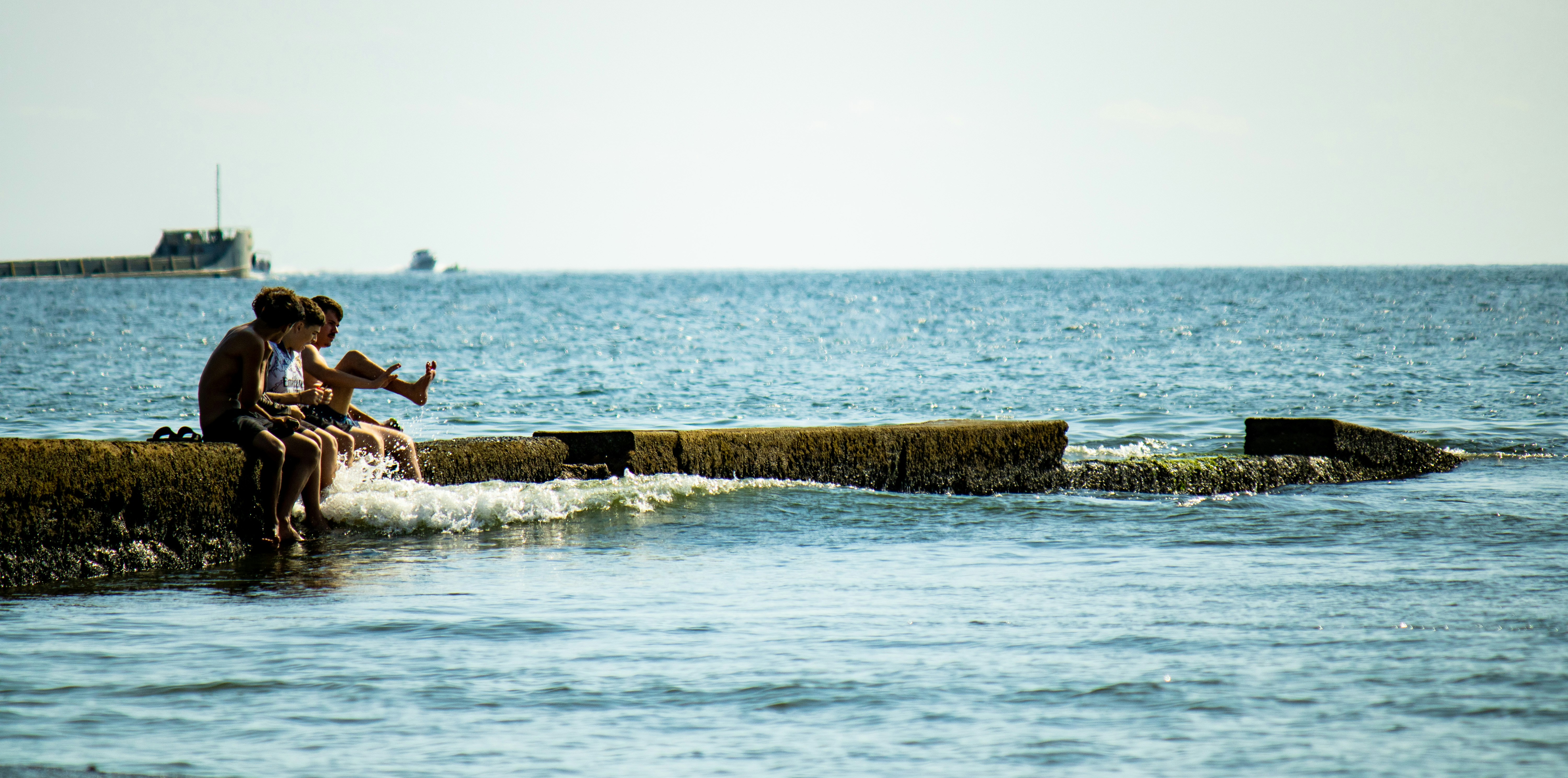 Two people seated on a weathered stone bridge extending into the sea, gazing at the horizon.