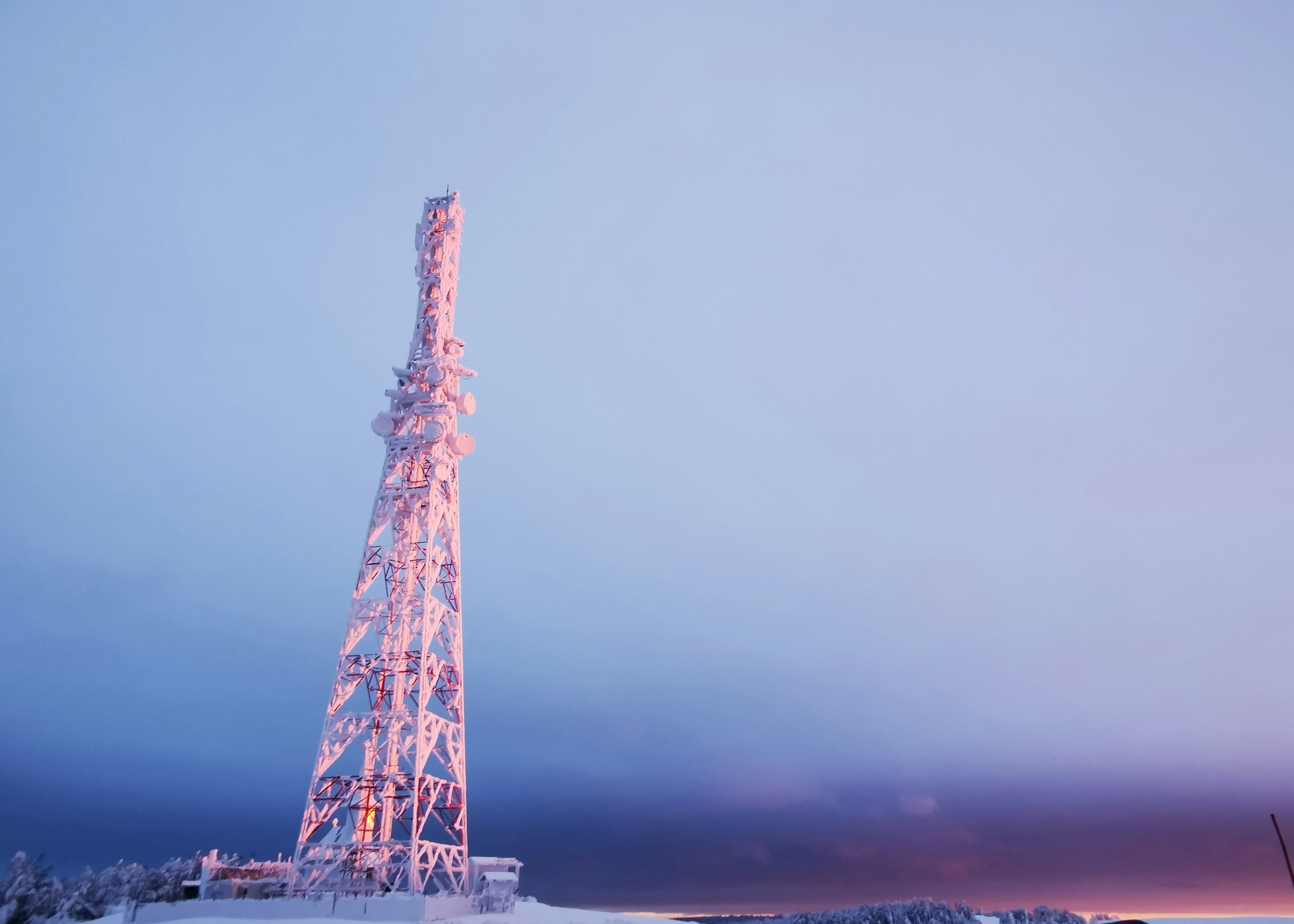 Tall communication tower encrusted with ice, illuminated by soft twilight hues against a serene evening sky.