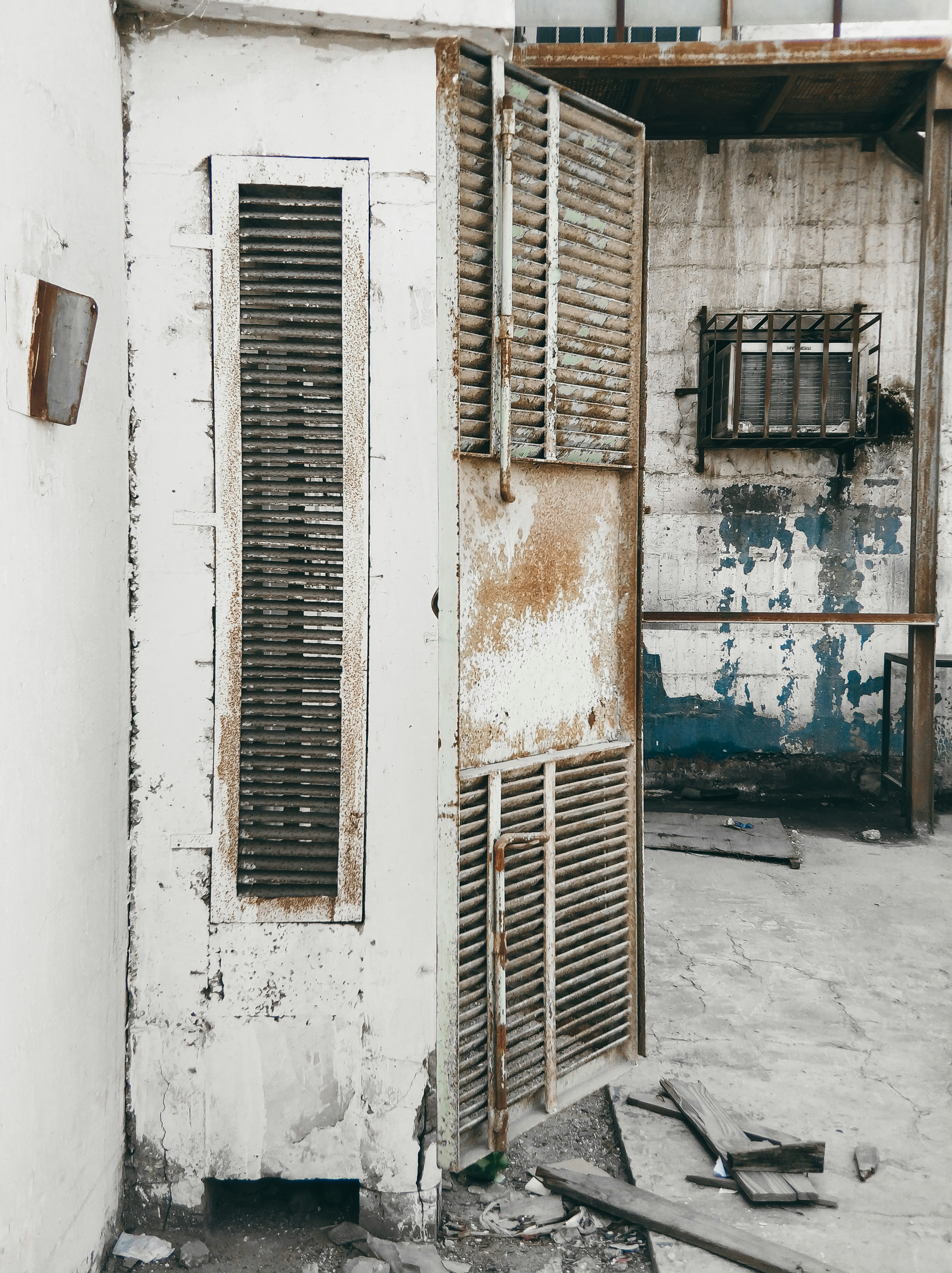 Rusty double doors stand ajar in a dilapidated interior, revealing peeling paint and remnants of a bygone era.