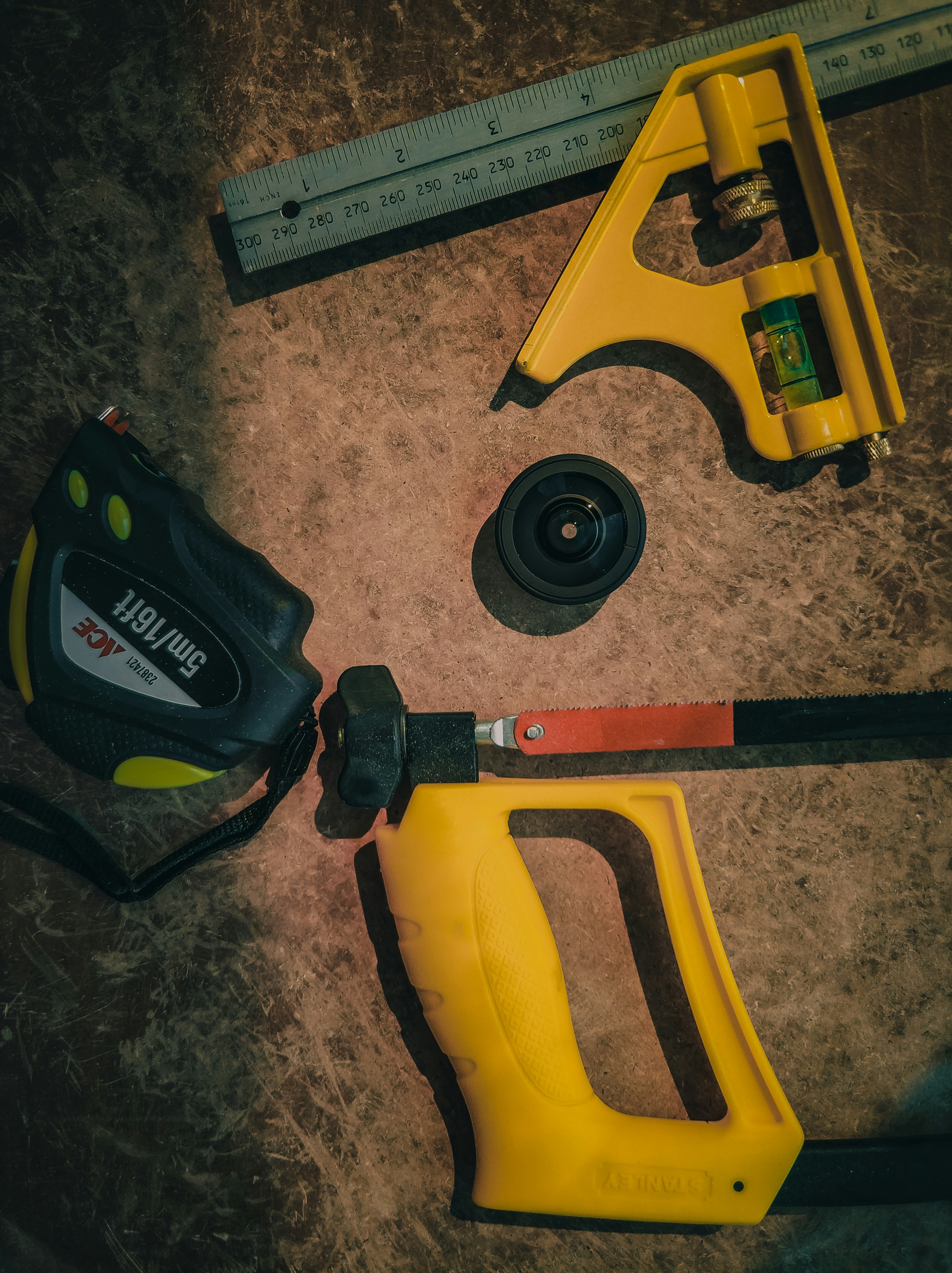 Close-up of yellow measuring tools and a ruler on a textured work surface, with a central circular lens-like element drawing focus.