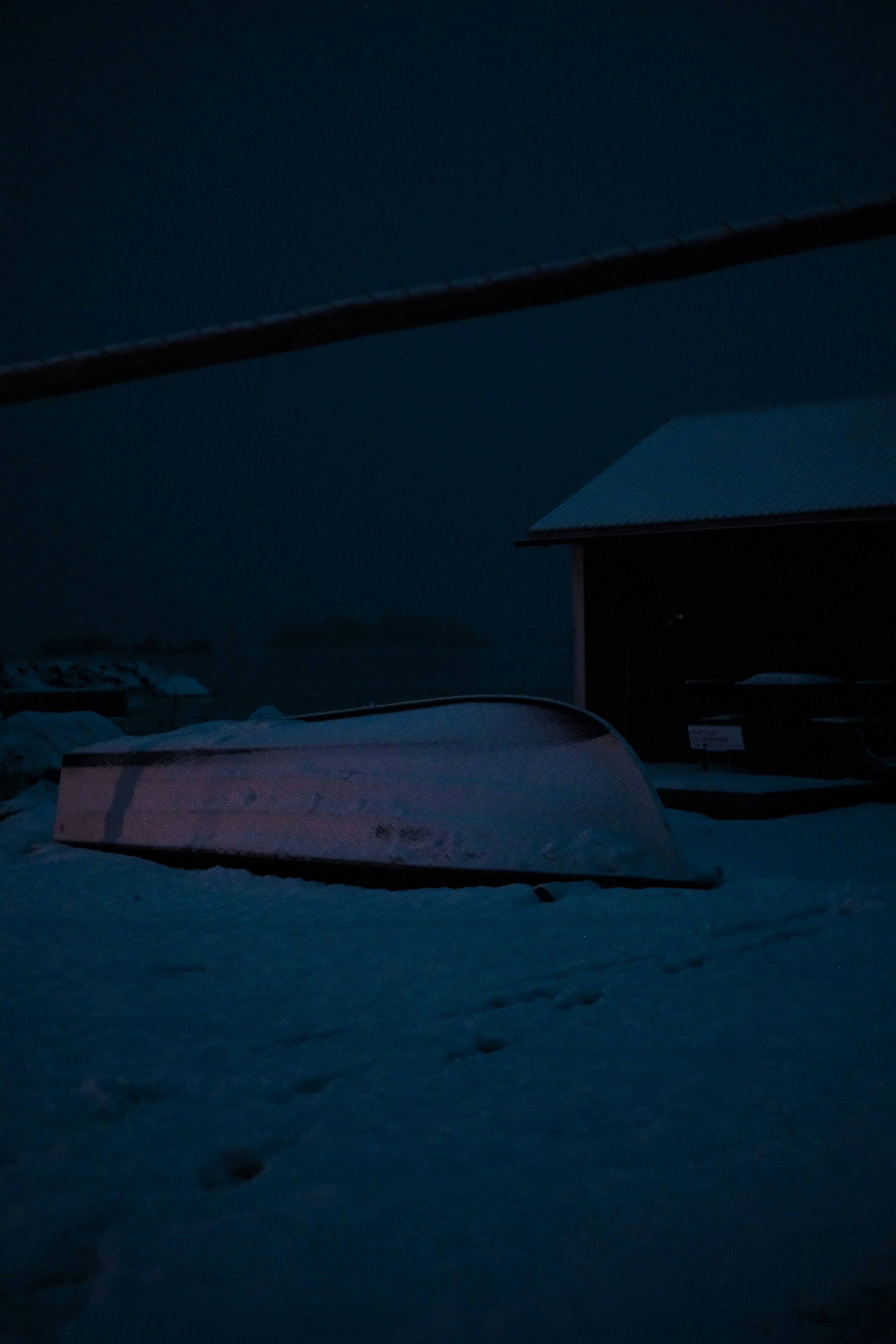 Blue Hour Stillness: A Snow-Covered Boat Beside a Silent Boathouse