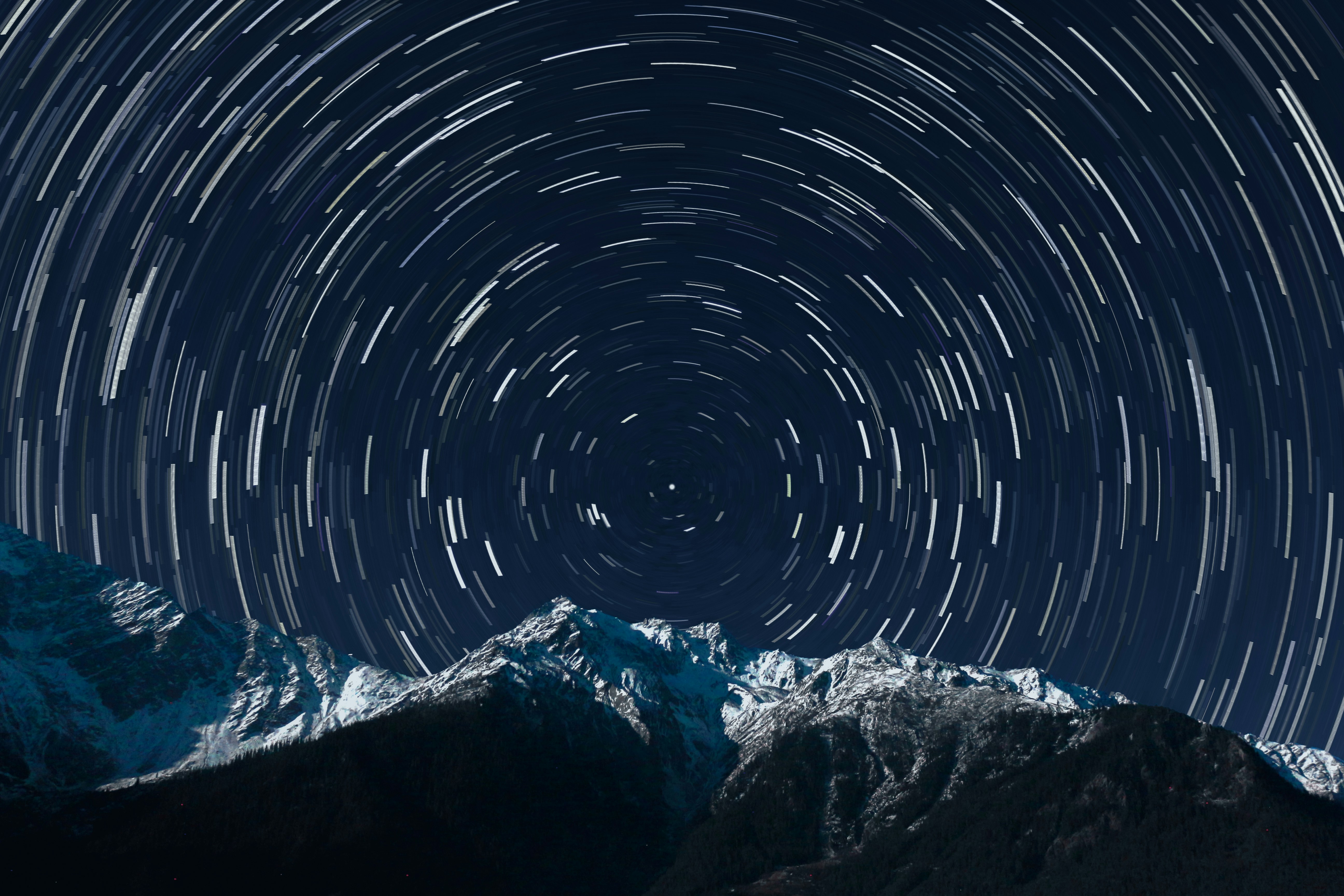 A star trail is seen in the sky above a mountain range photo – Free ...