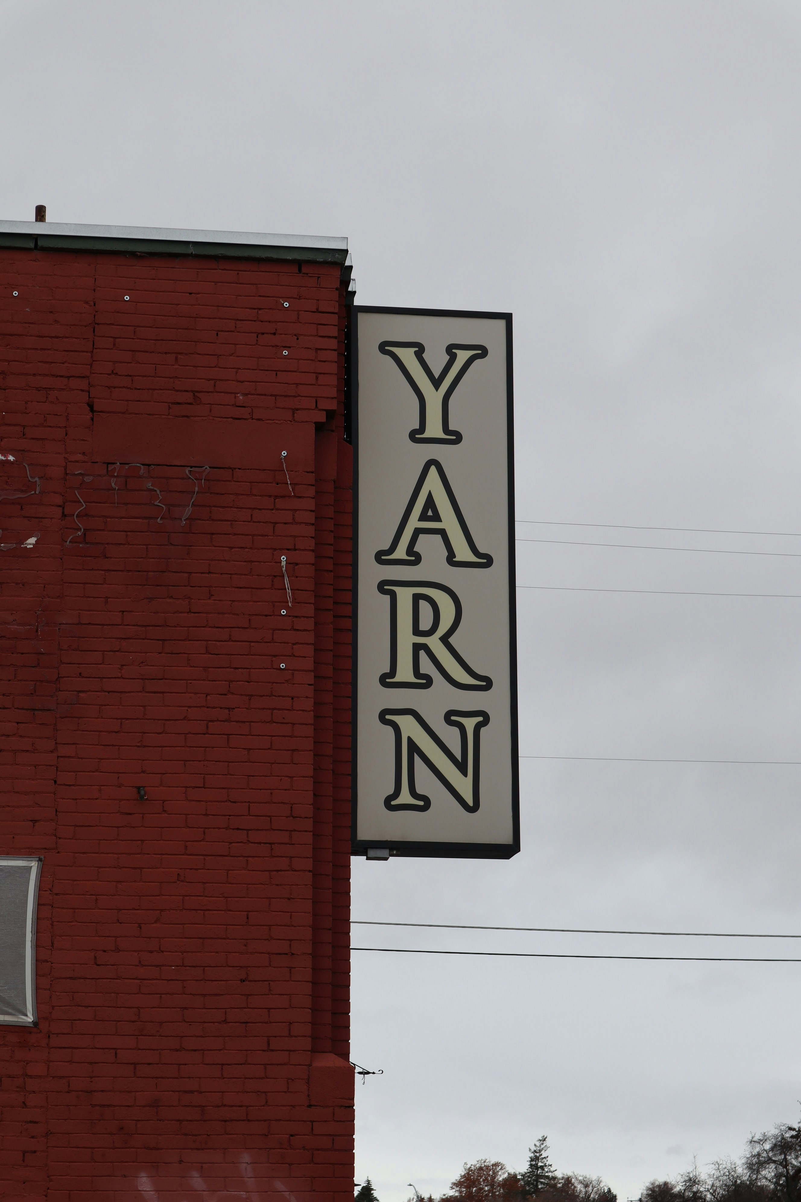 Vertical Signpost: YARN on a Red Brick Facade