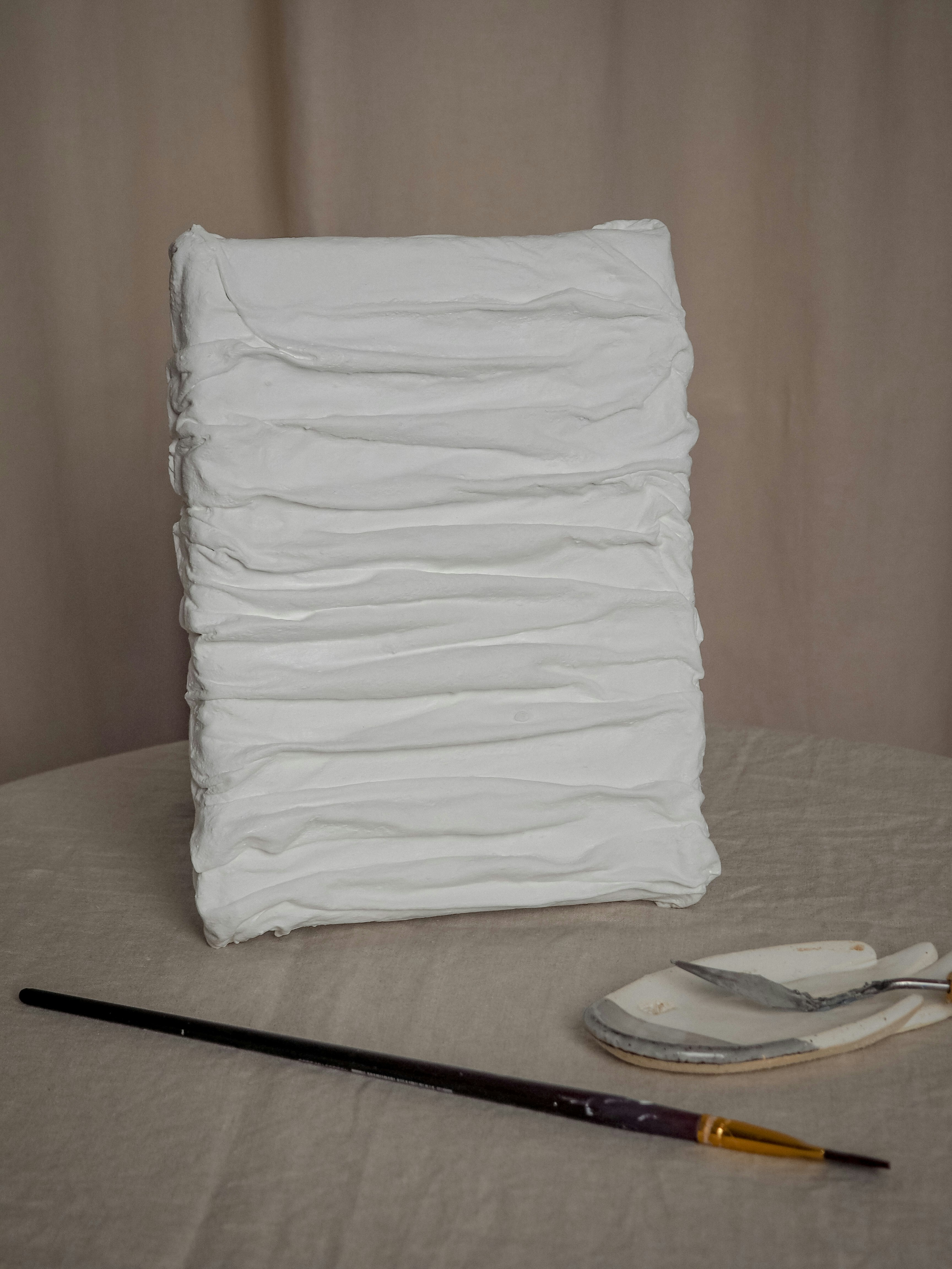 A stack of white cloth sitting next to a paintbrush photo – Free ...