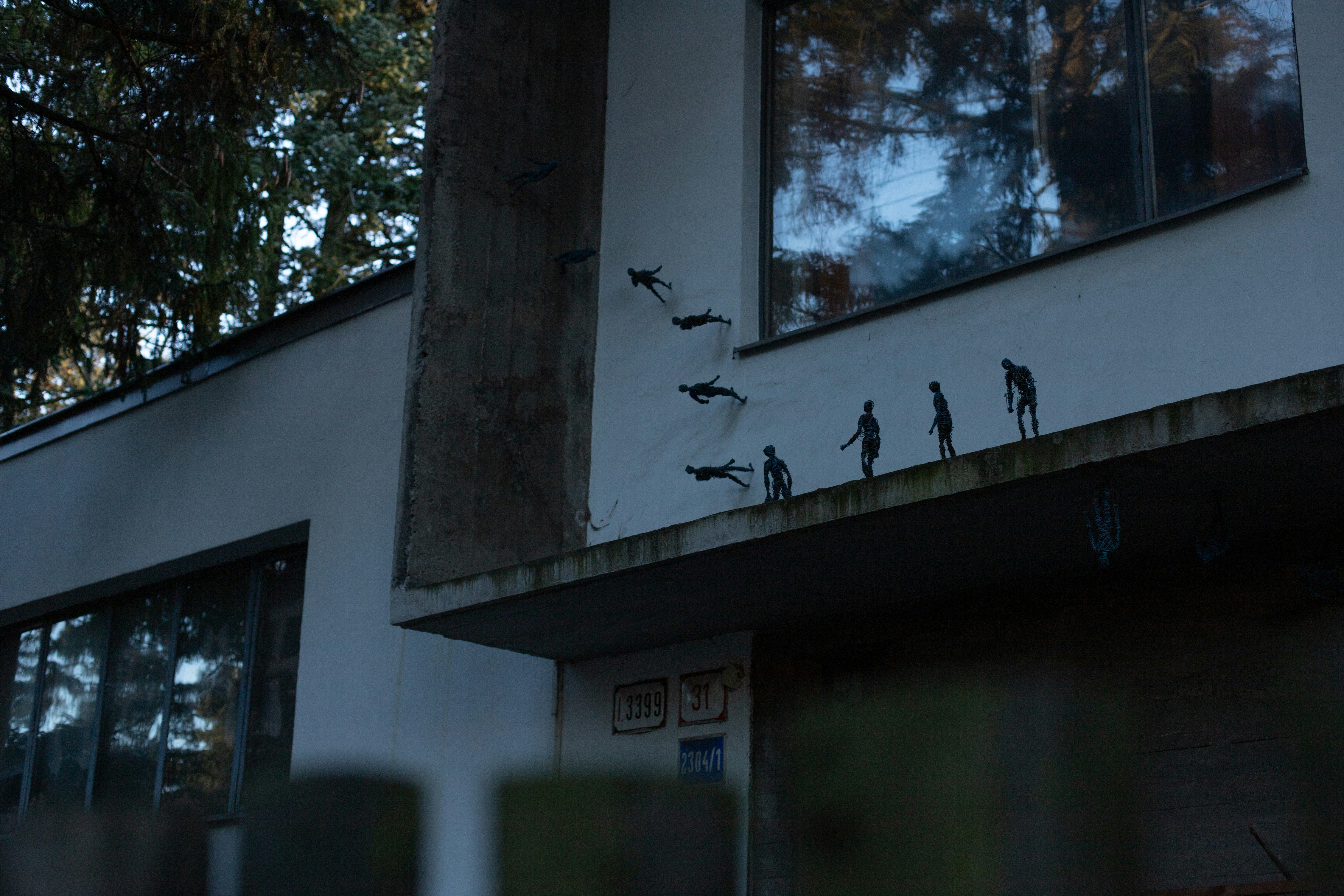 Line of shadow figures tracing a concrete balcony across a modern facade at dusk