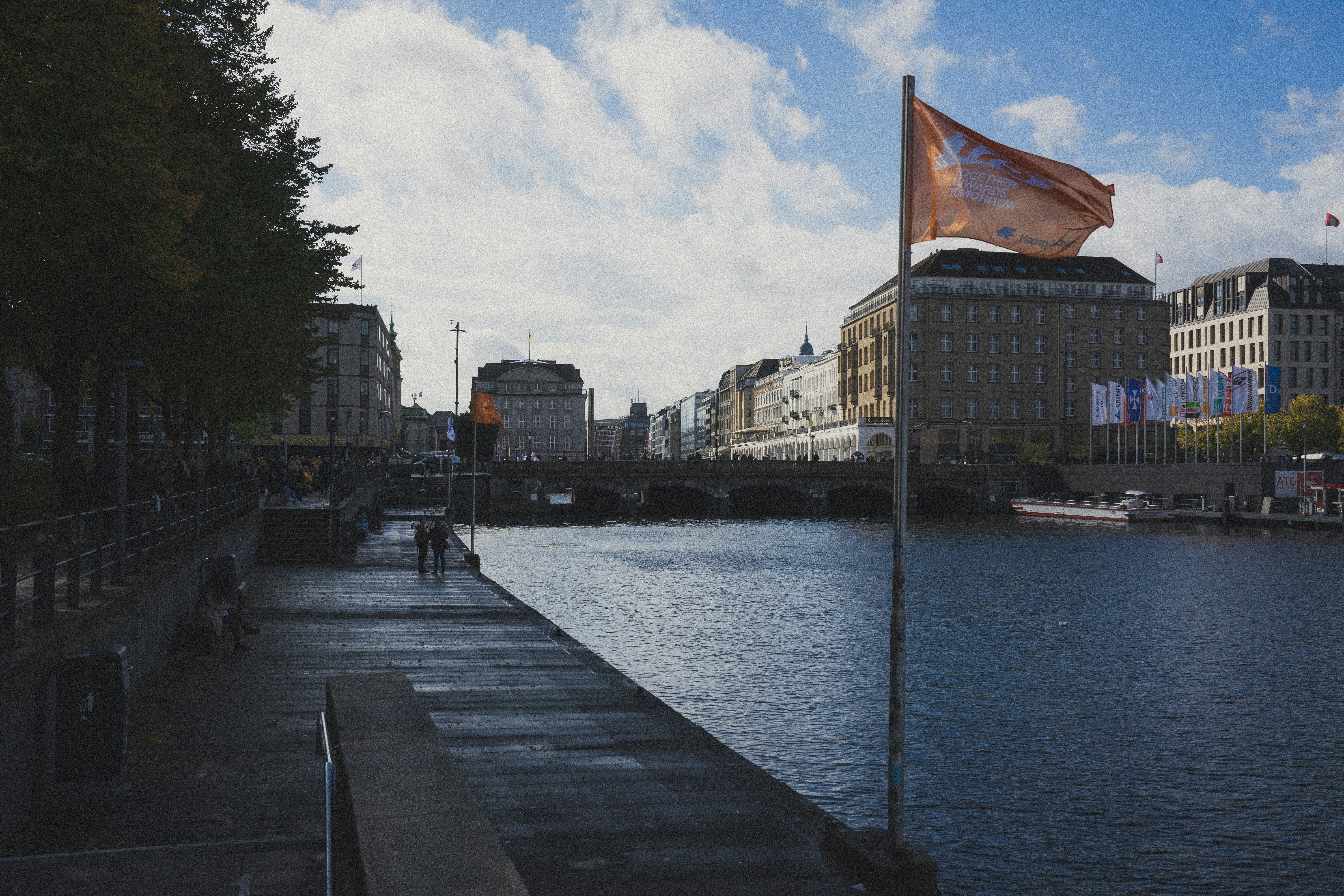 Flagpole on a Sunlit City Quay Overlooking a Calm Canal and Arched Bridge