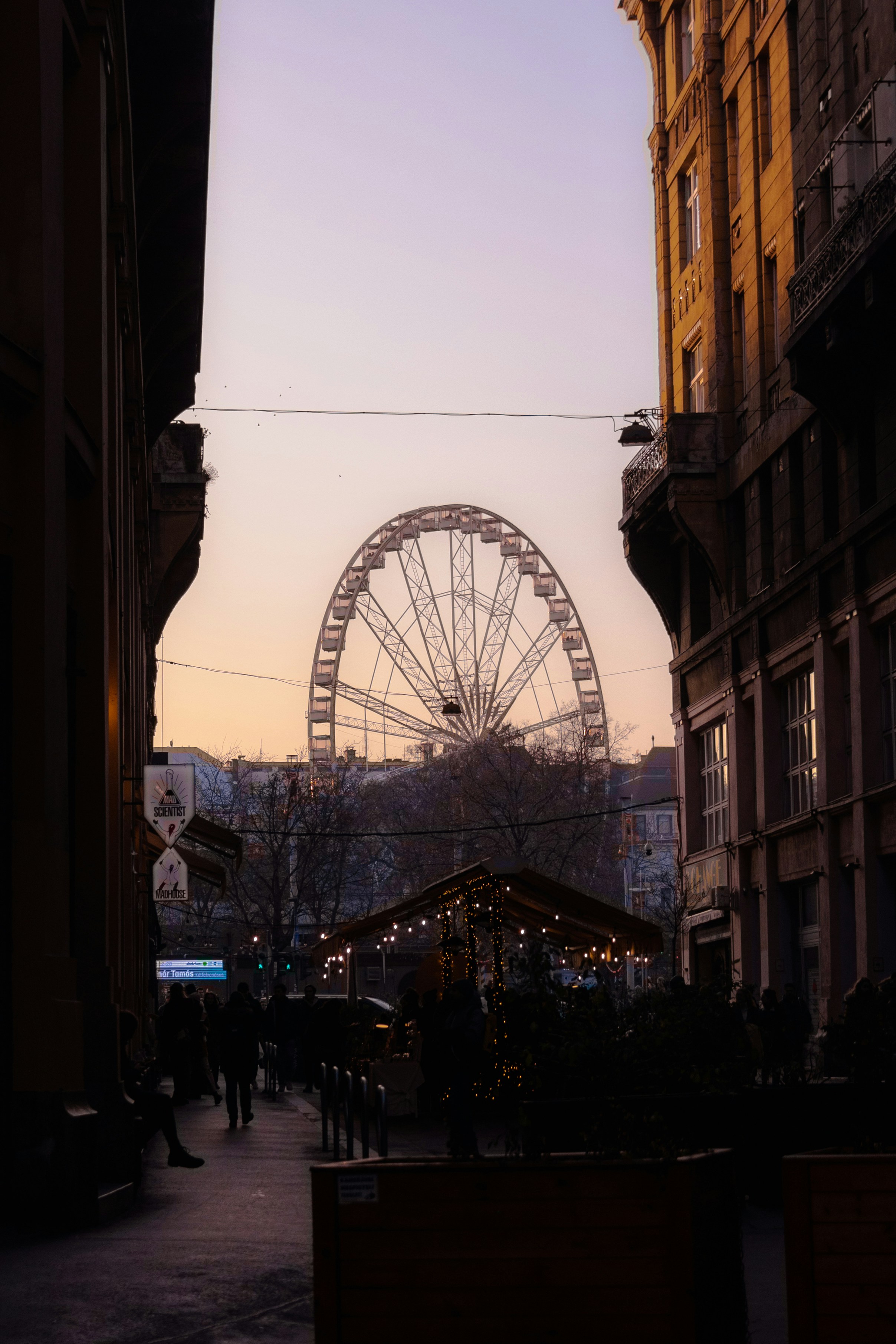Dusk Through the Archways: Ferris Wheel Rising Over a Quiet City Street