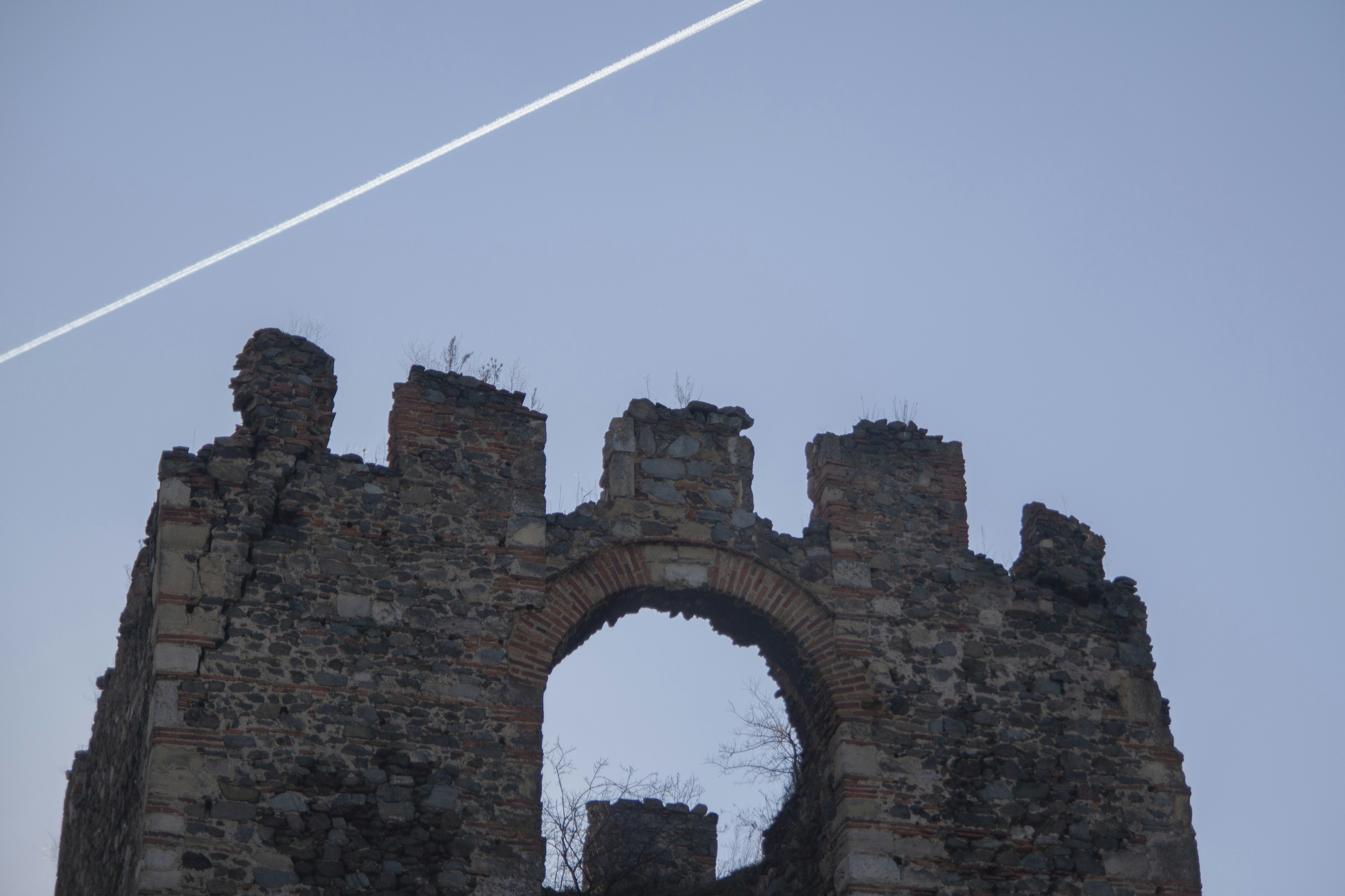A plane flying over a castle wall with an arch photo – Free Building ...