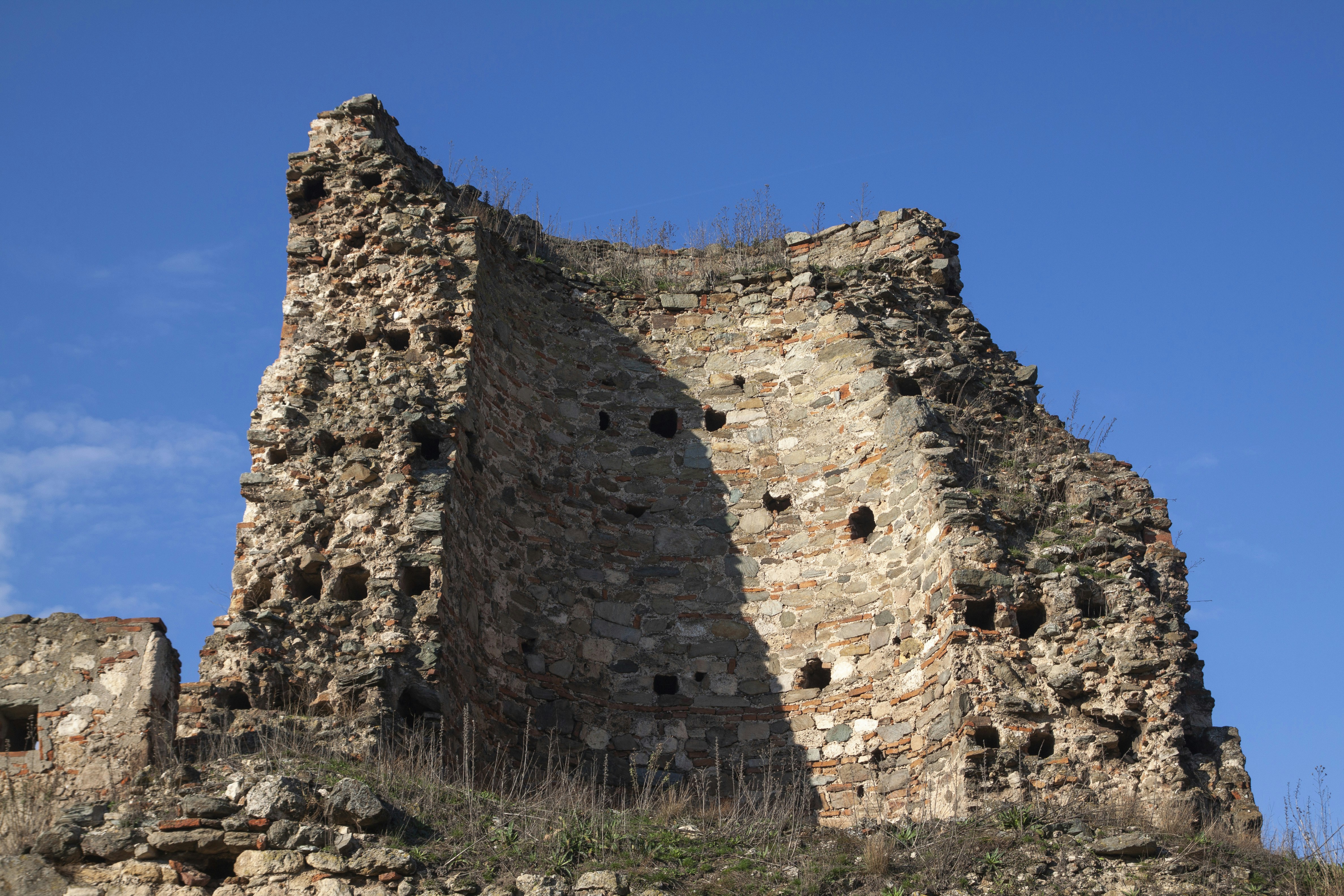 Ancient stone ruin with rugged texture standing tall under a clear blue sky.