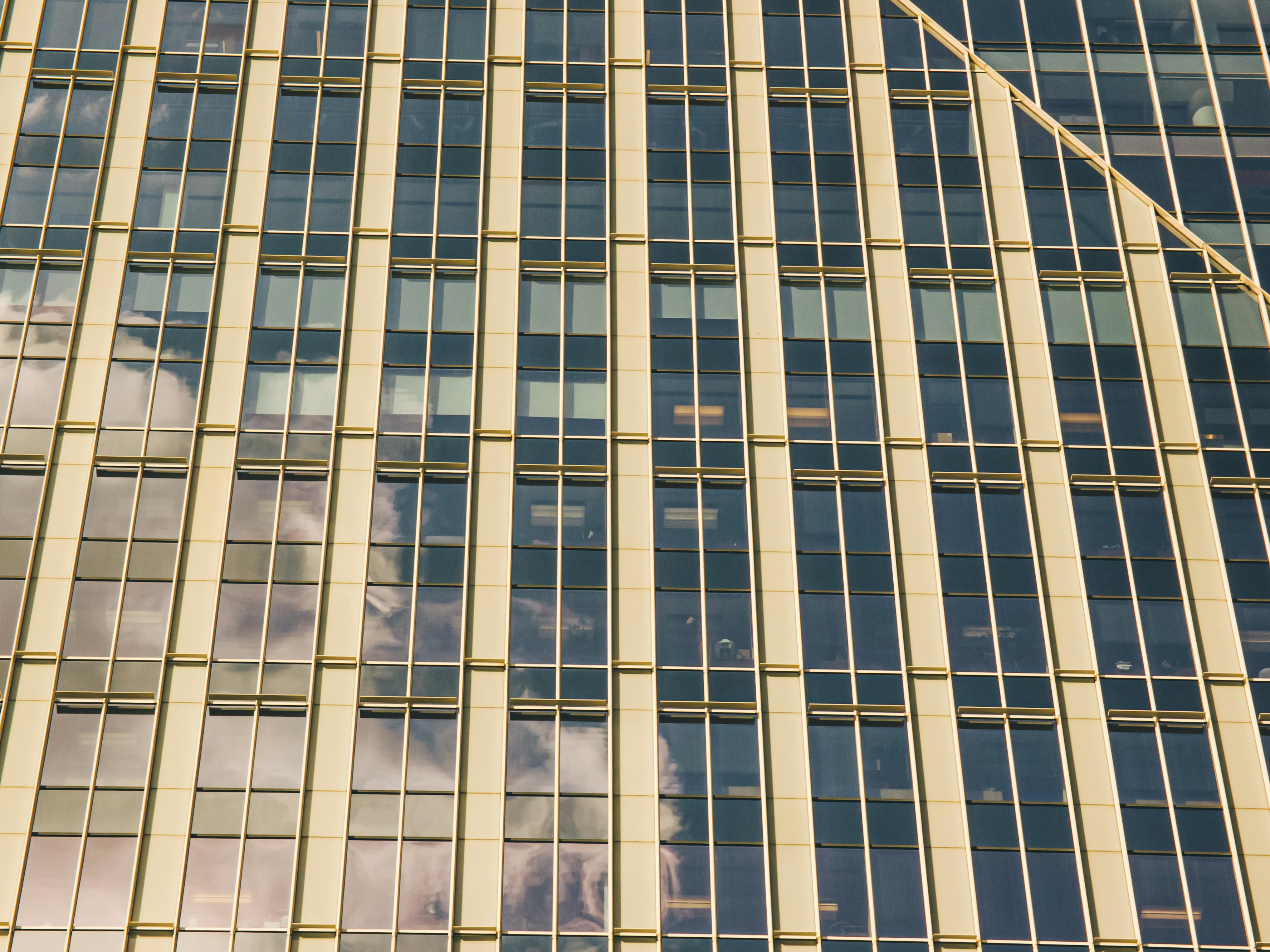 Glass-clad office building facade with vertical mullions and diagonal cables catching the light.