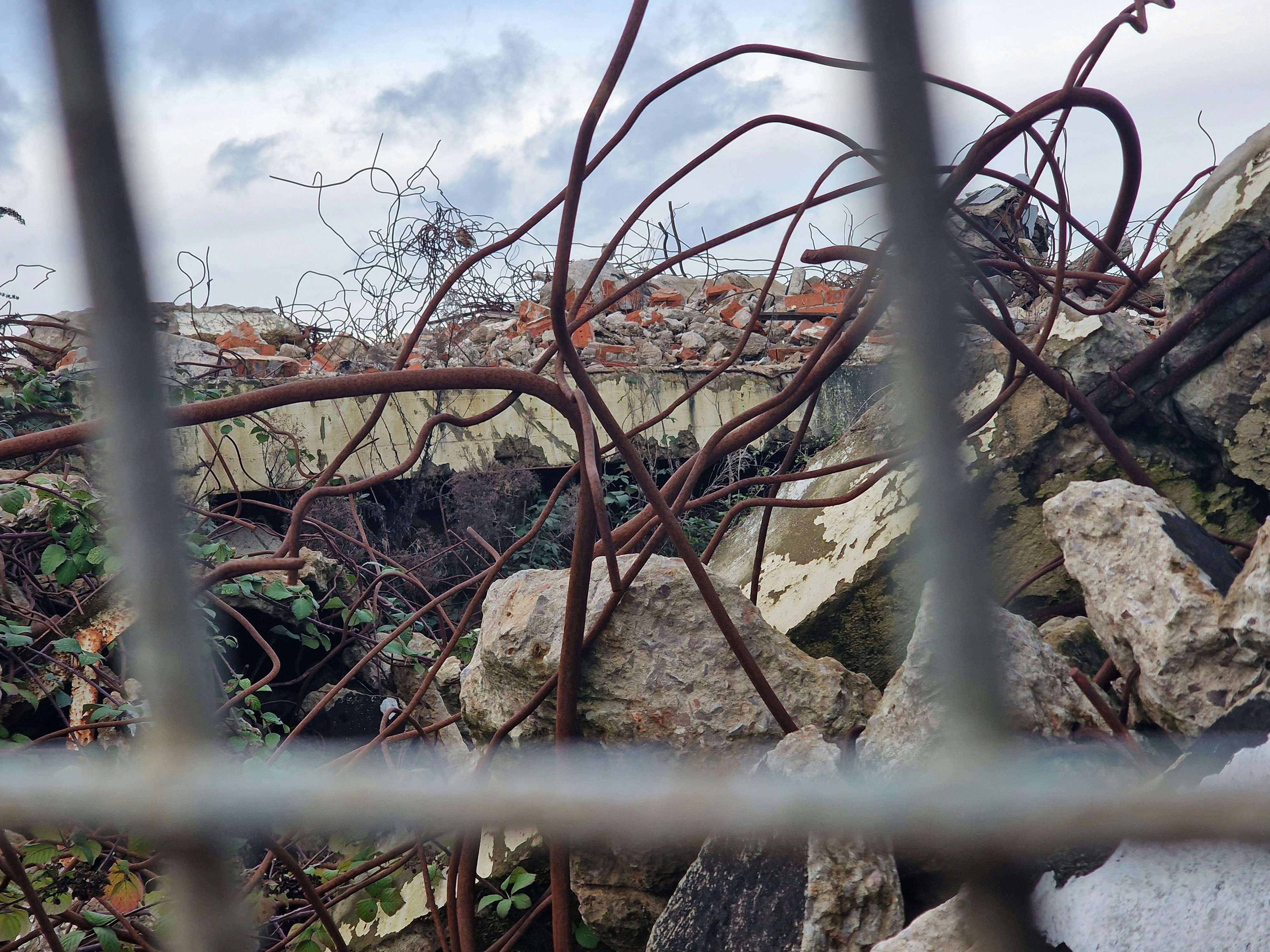 Rusted Web Over Rubble: A Fence-Framed Moment