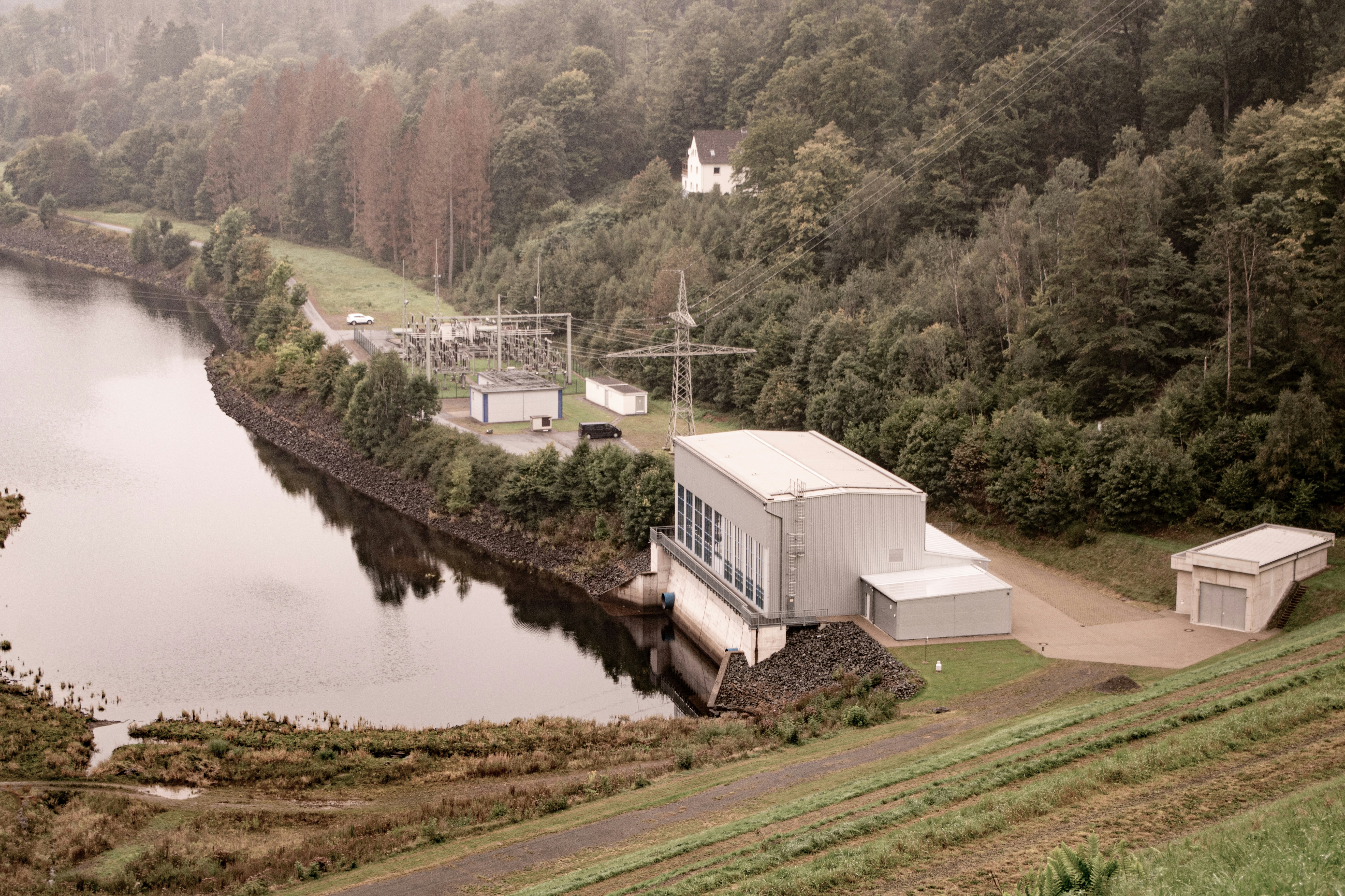Hydroelectric facility nestled beside a calm river and surrounded by lush forest.