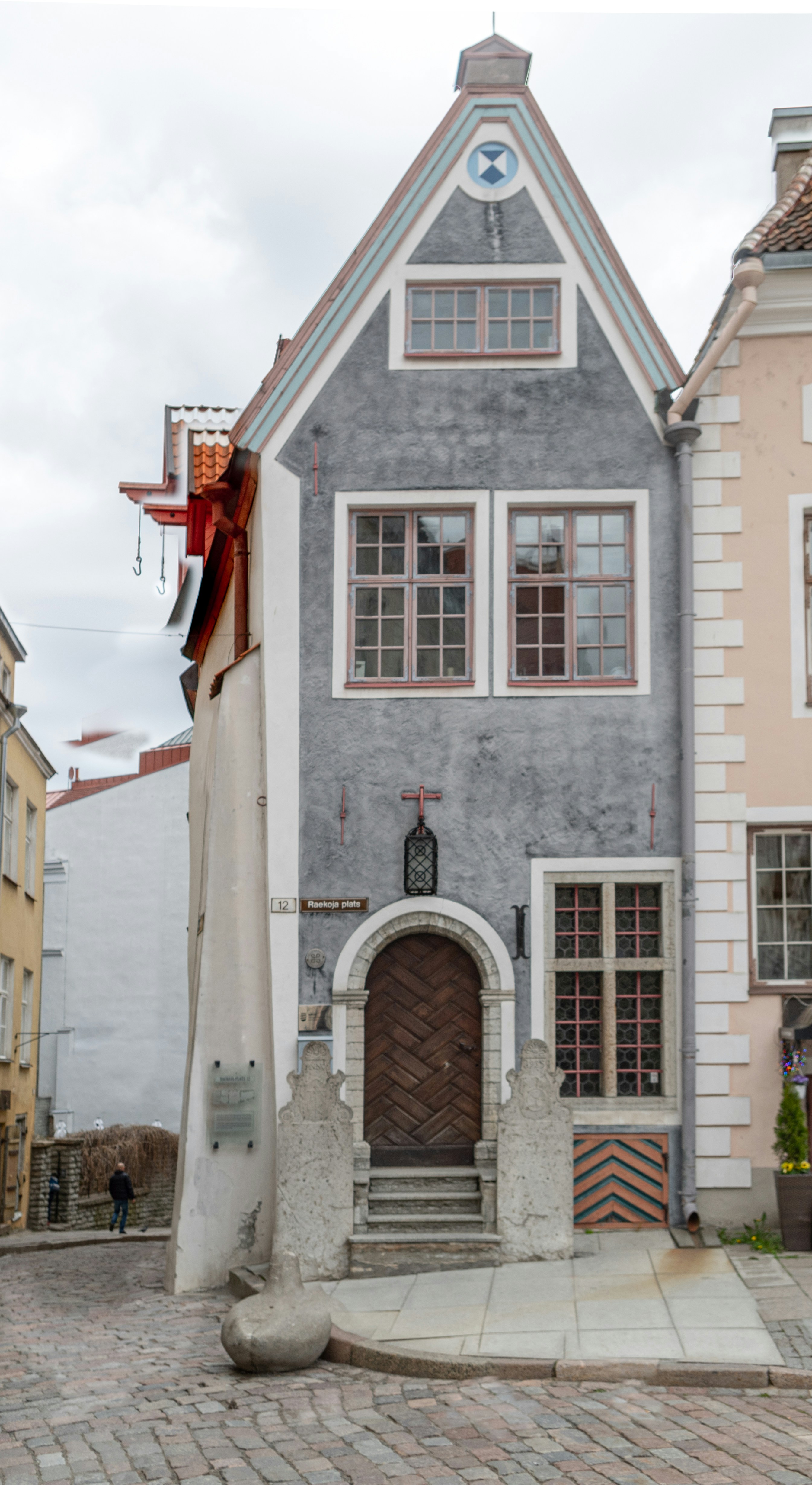 Historical building featuring a distinct gray facade and ornate wooden door, set against the cobblestone street of Tallinn.