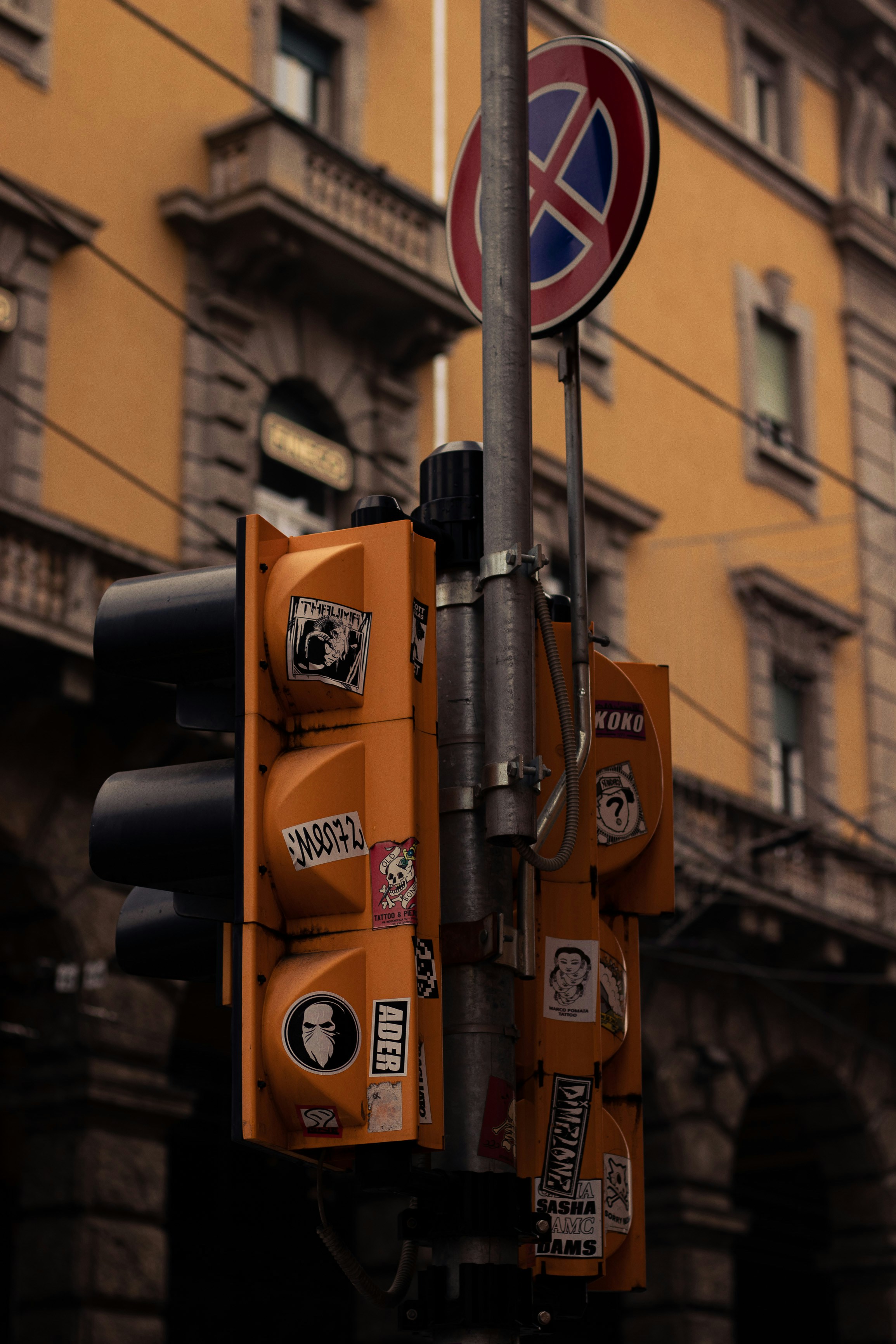 Stickered Orange Traffic Signal Anchored by a European Street Facade