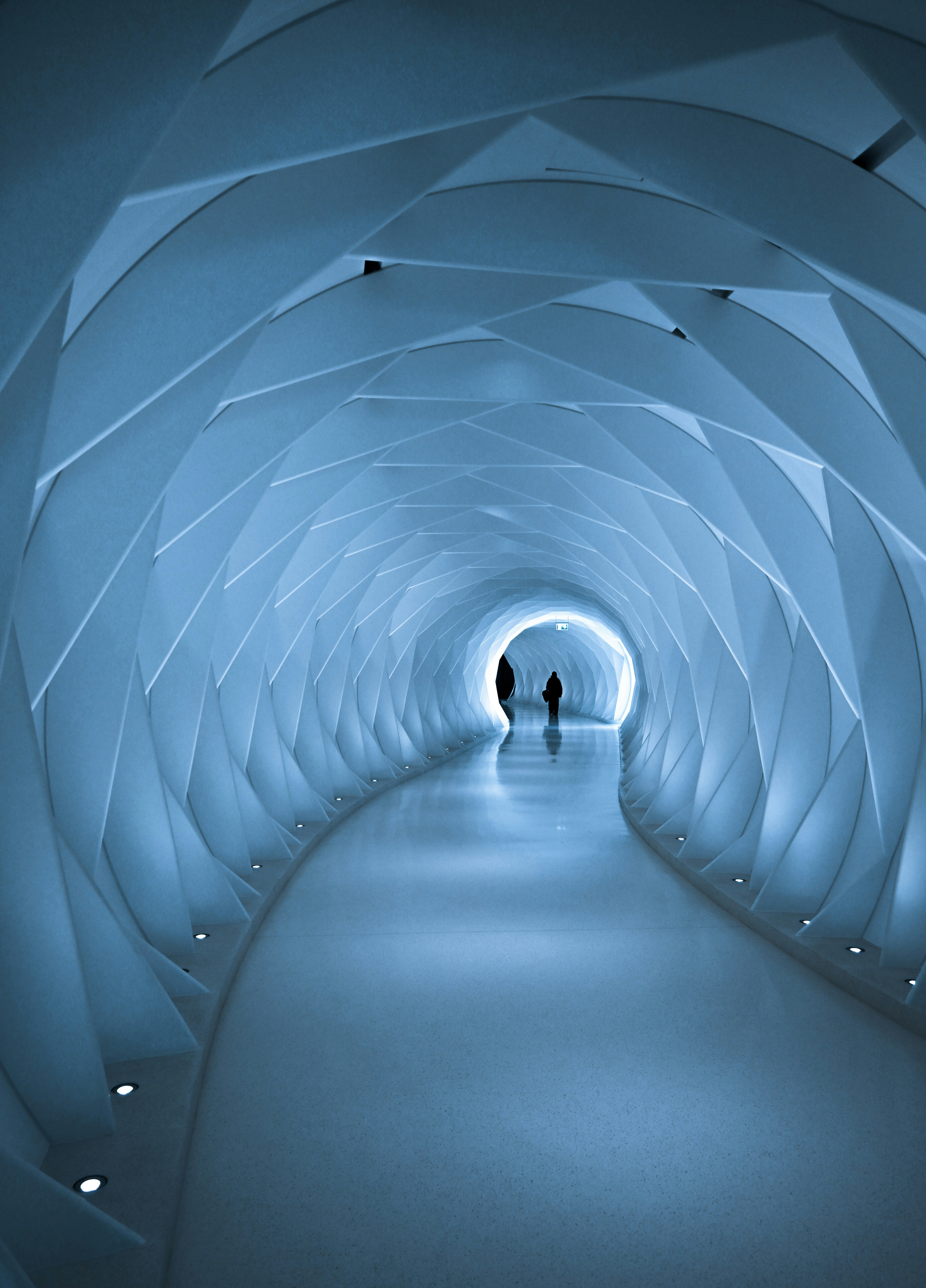 Cobalt Arches: A Lone Figure Traverses the Geometric Tunnel Toward Light