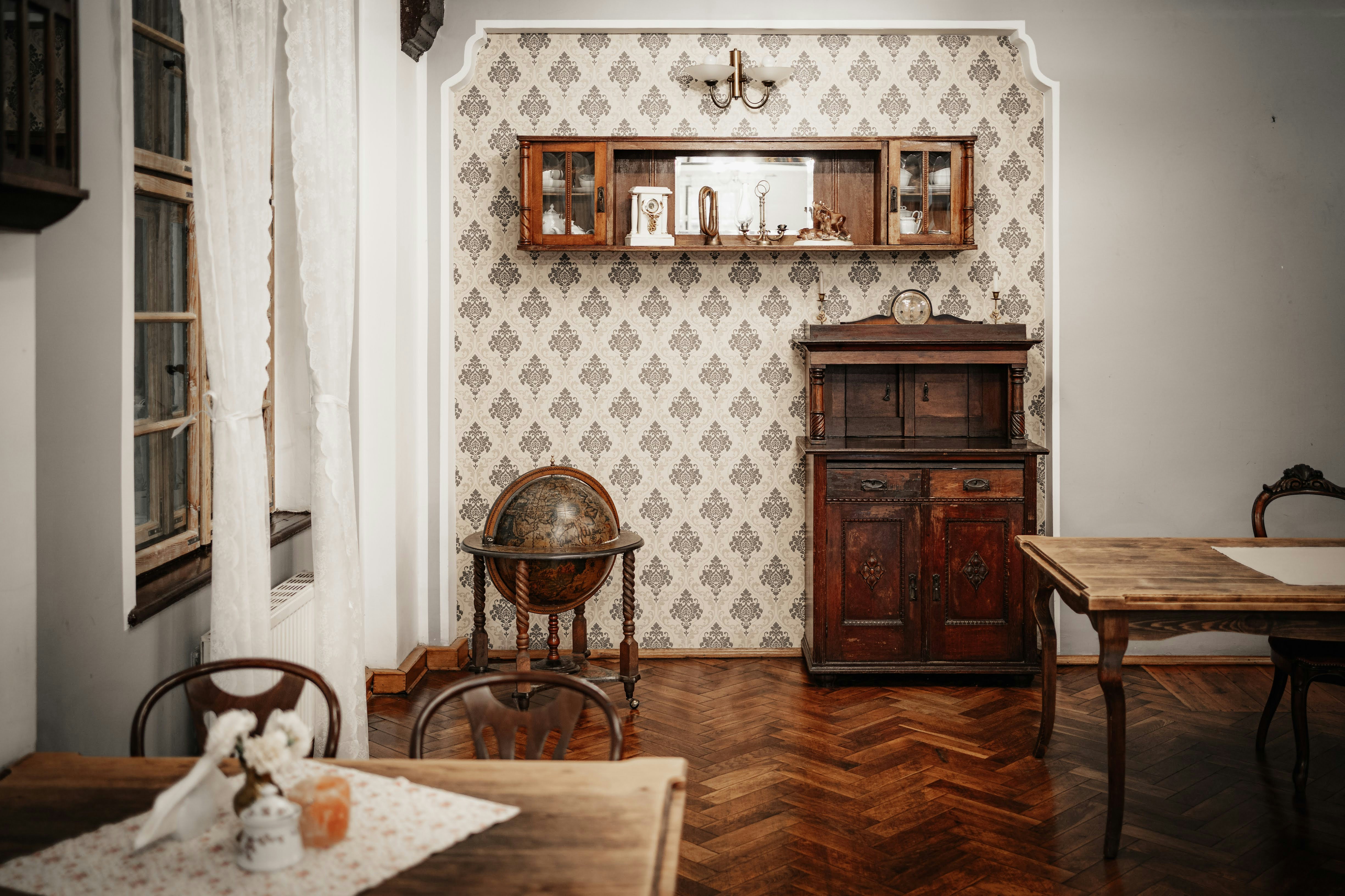 Cozy interior featuring antique furniture, a wooden globe, and a patterned wall, creating a nostalgic atmosphere. The arrangement invites a sense of warmth and history.