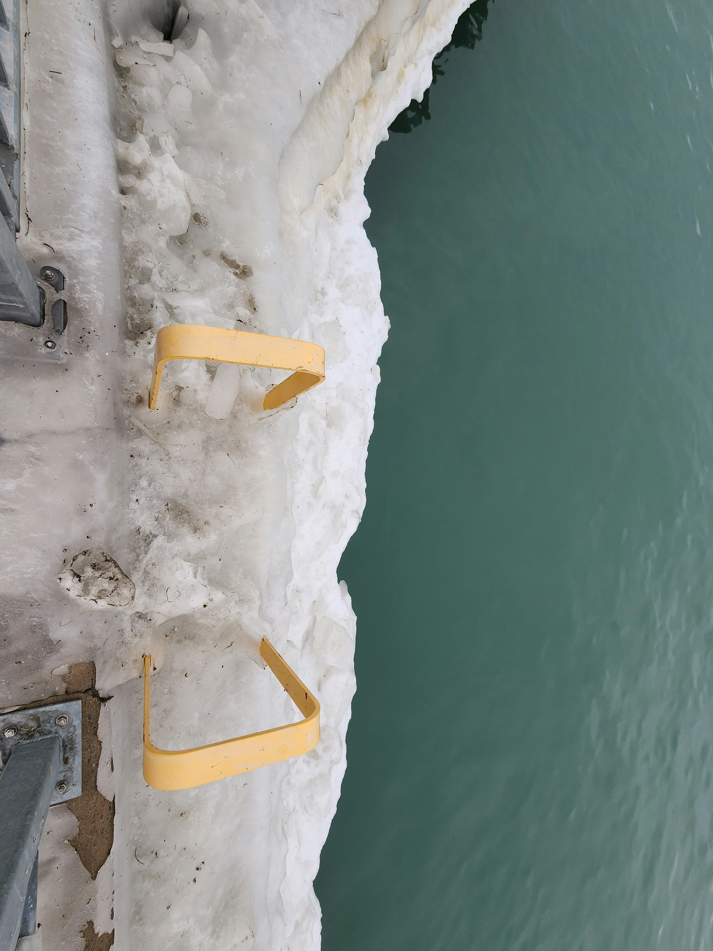 Yellow railings contrast against icy edges by the water's surface, capturing a moment of winter's chill. The serene water reflects a muted palette.