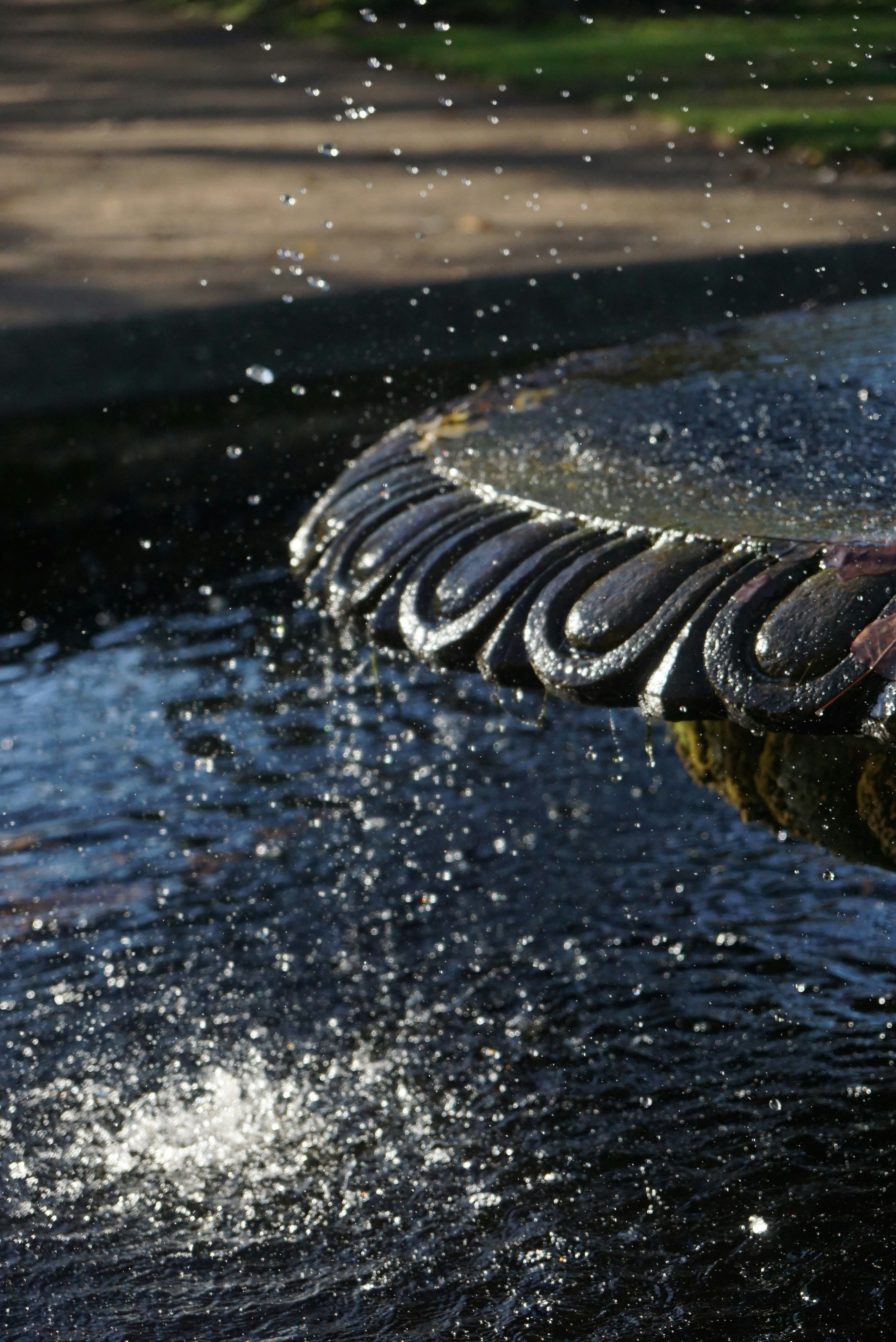 Edge of a stone fountain with droplets of water splashing in the pond | a close up of a bird bath in a body of water