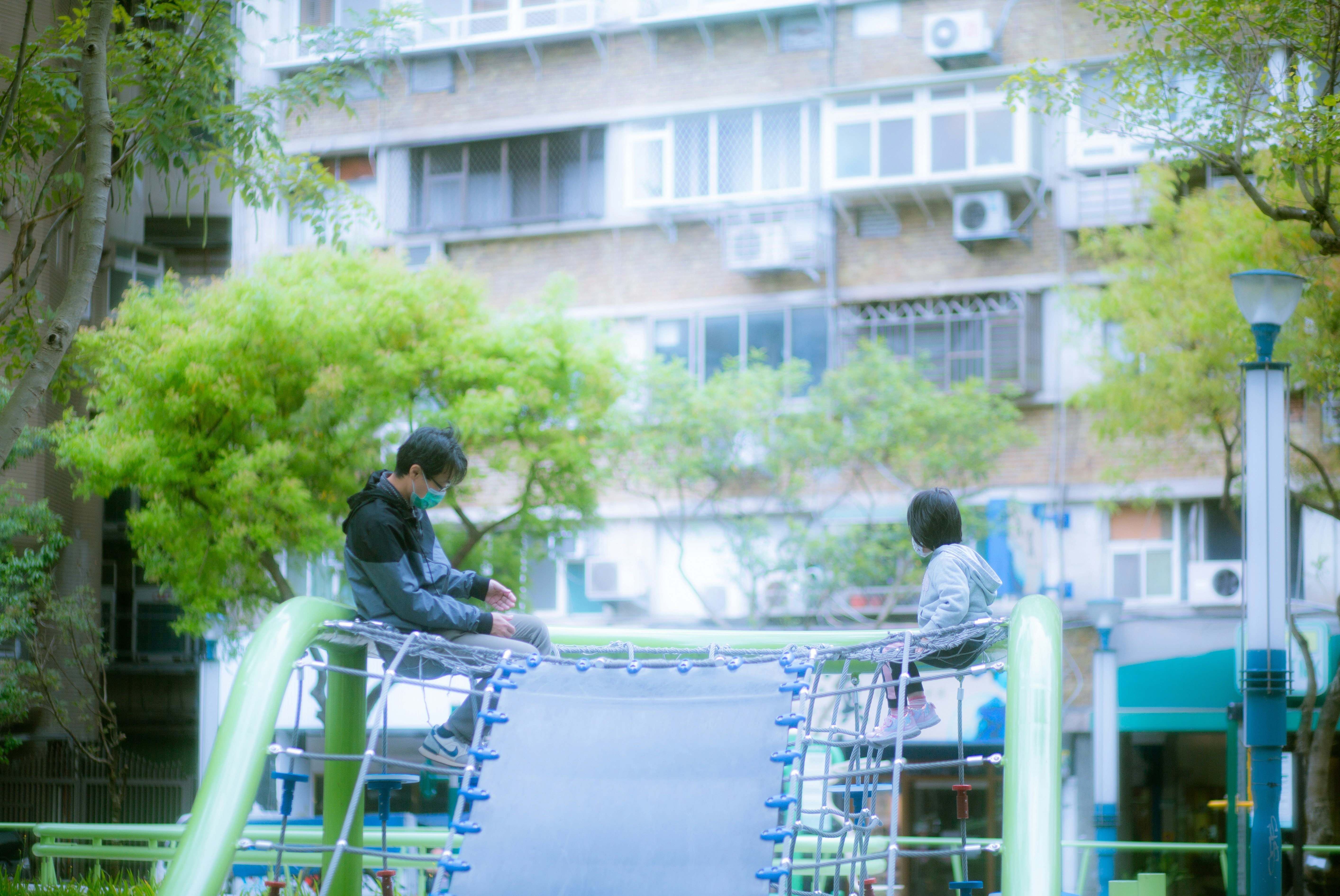 Two figures at the edge of a bright playground slide, framed against a residential backdrop