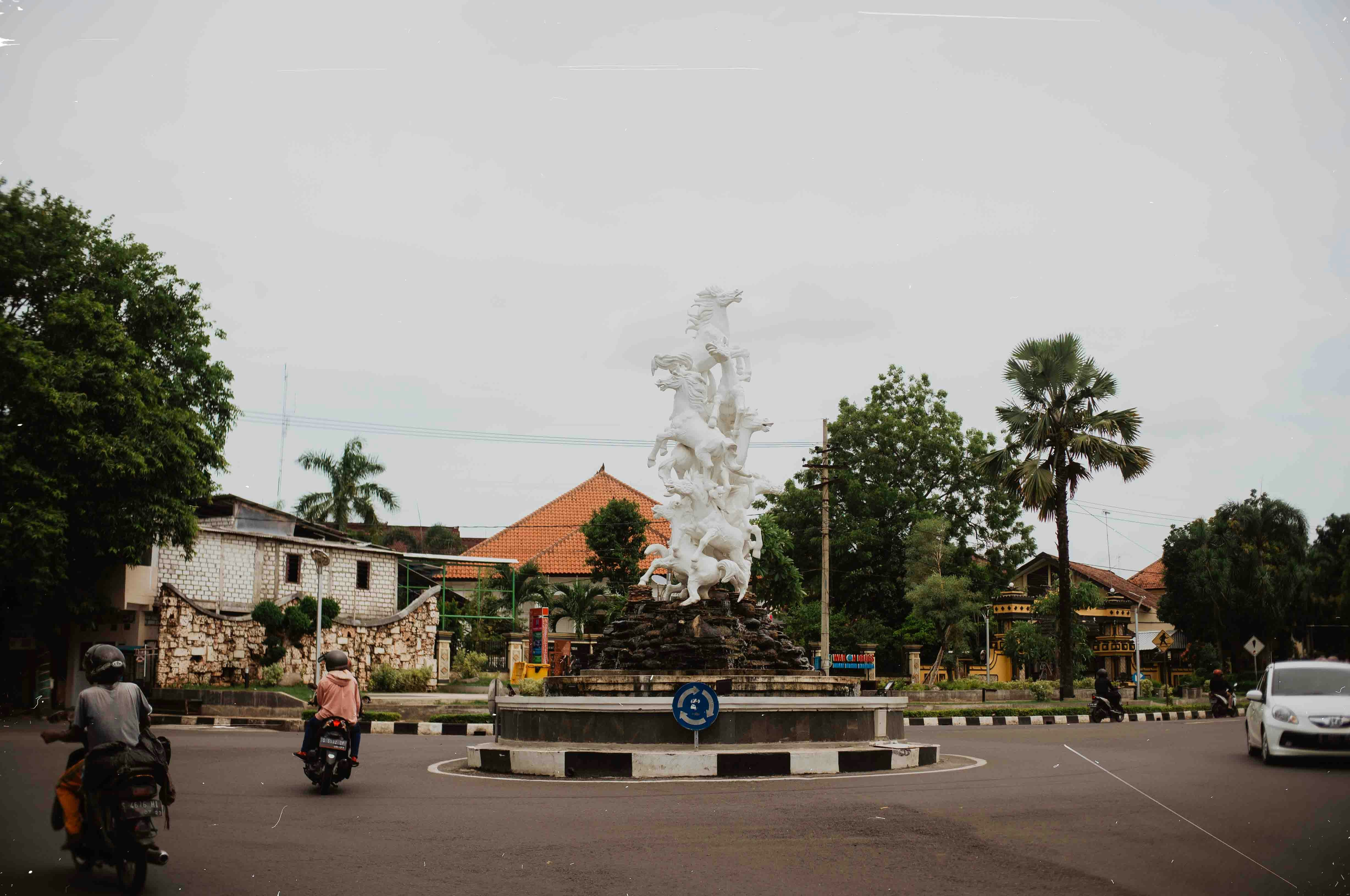 a man riding a motorcycle down a street next to a fountain