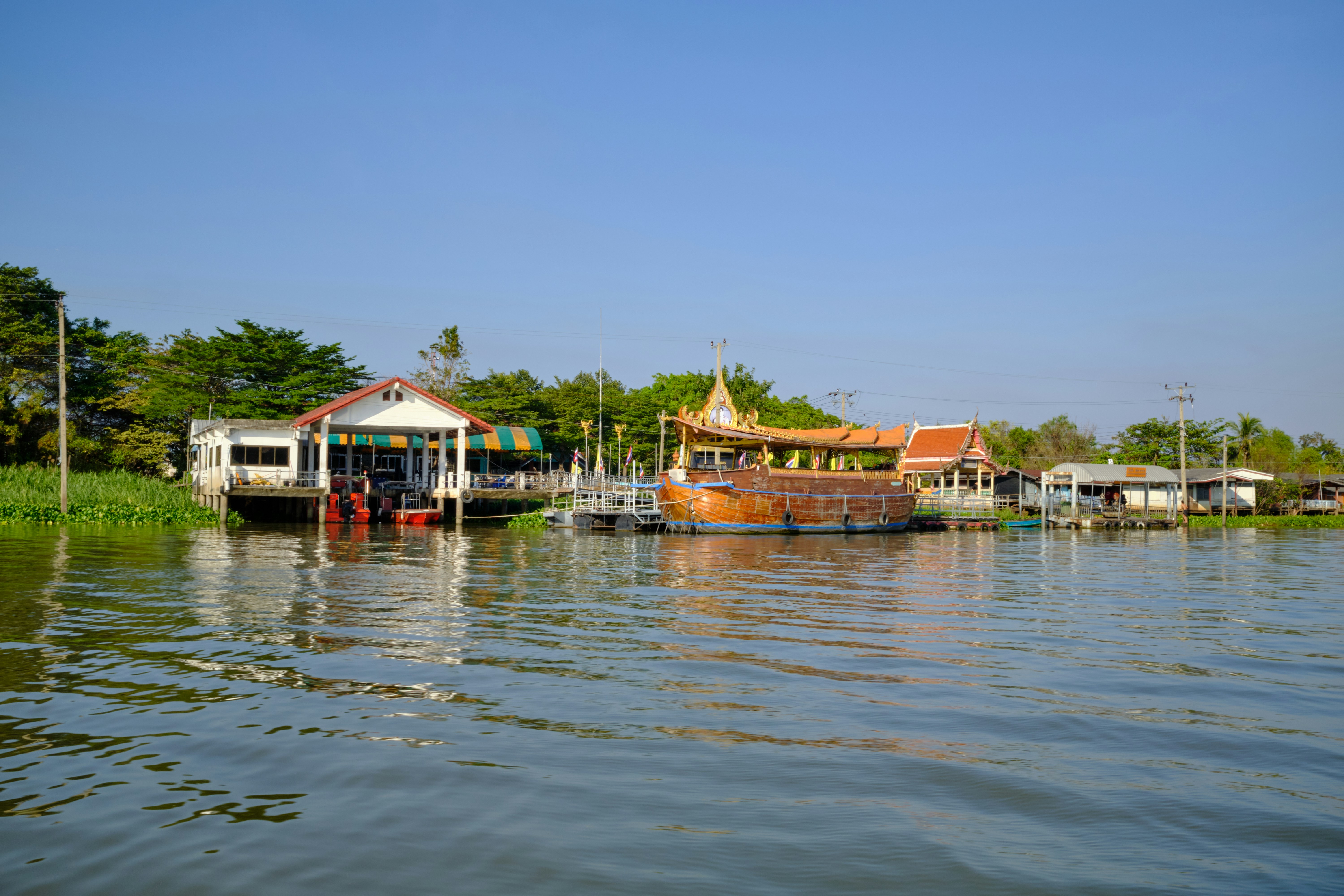 Traditional boats docked by colorful riverside houses under a clear blue sky.