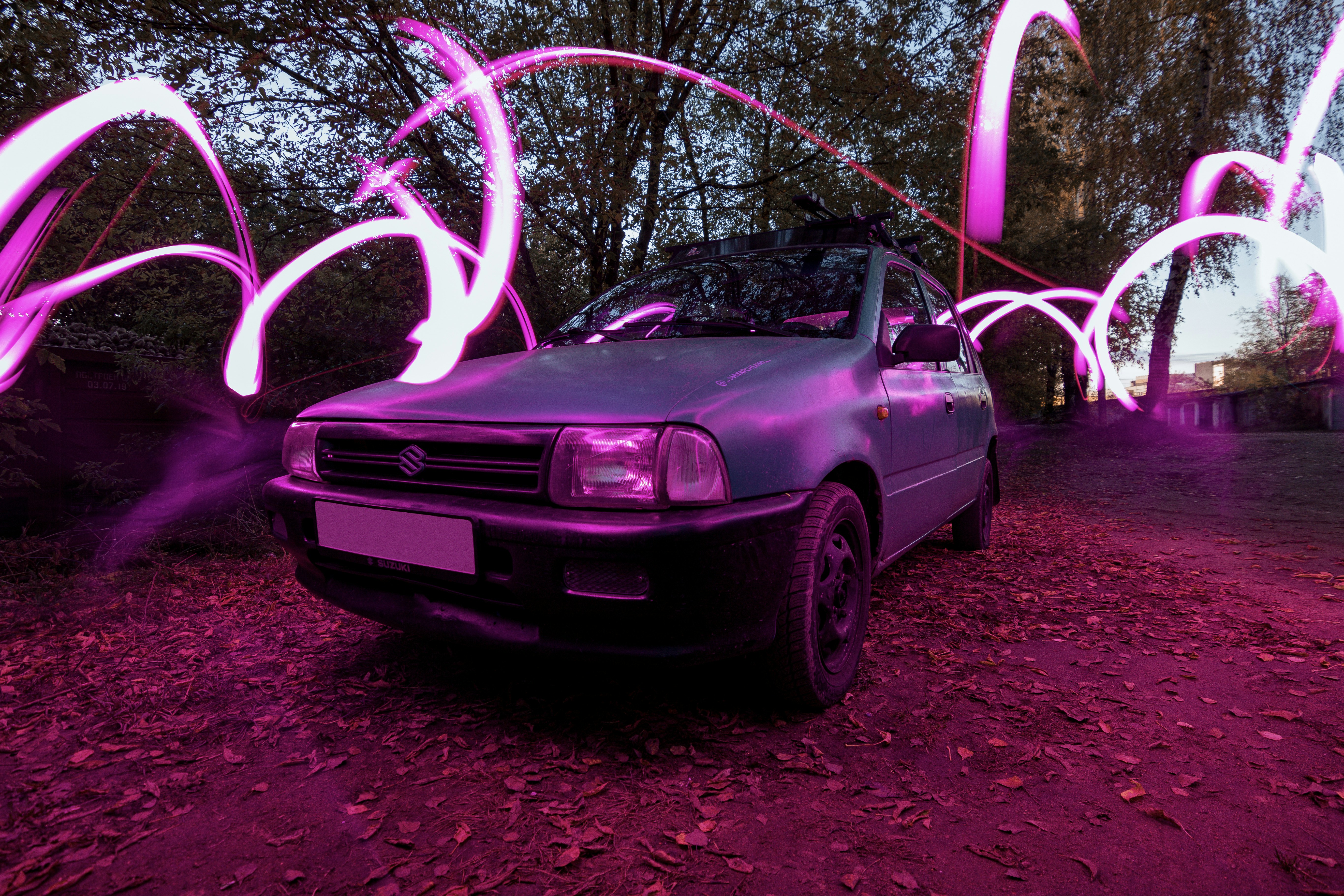 Car parked on a dirt road with vibrant pink light trails swirling around it.