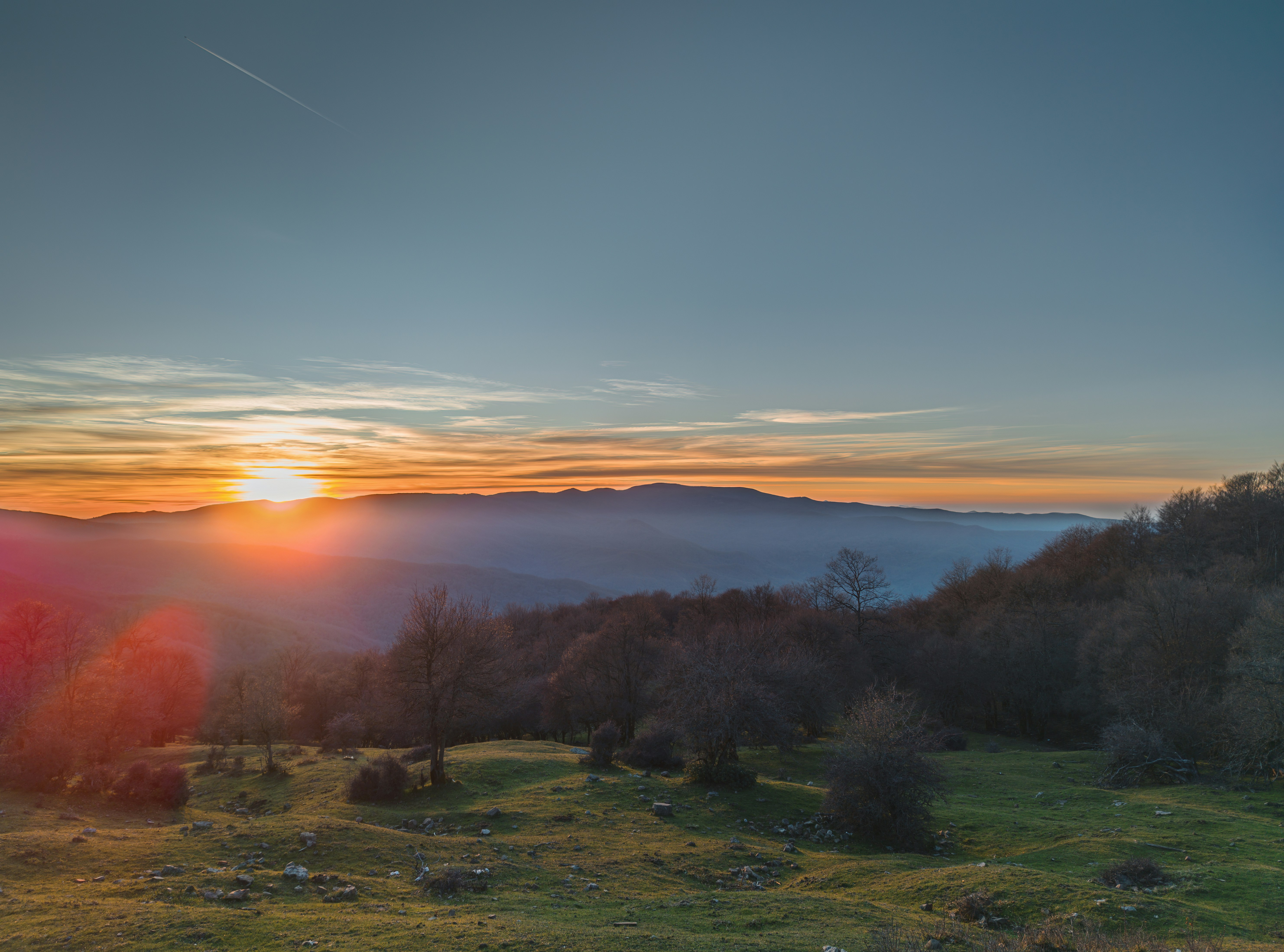 Landscape photograph of sunrise over rolling hills with a misty valley and scattered trees, bathed in warm, golden light.