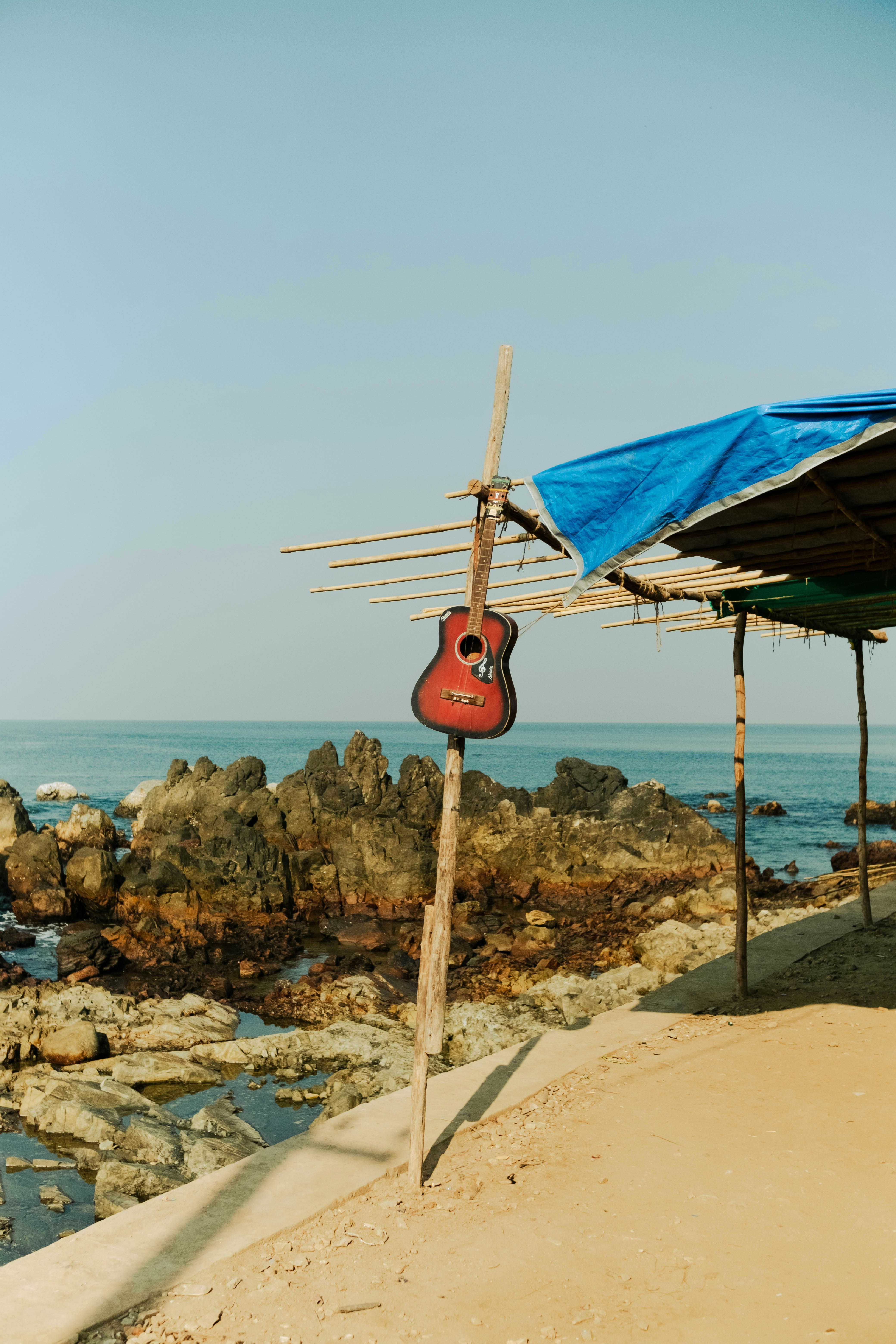 The Tide's Tuning: A Red Guitar on a Shorefront Post