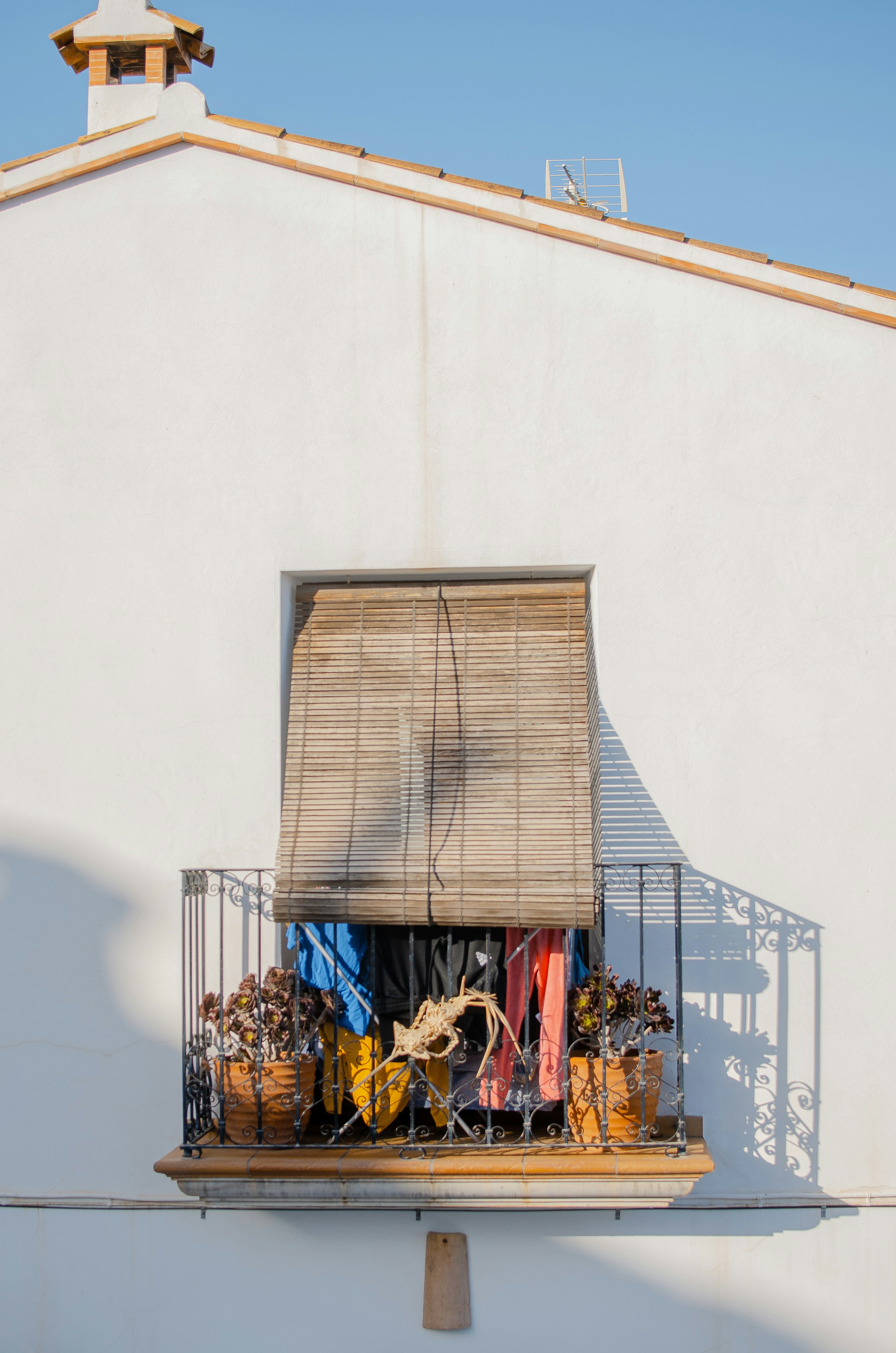 Sunlit Balcony: Colorful Fabrics and Potted Plants Behind a Bamboo Blind