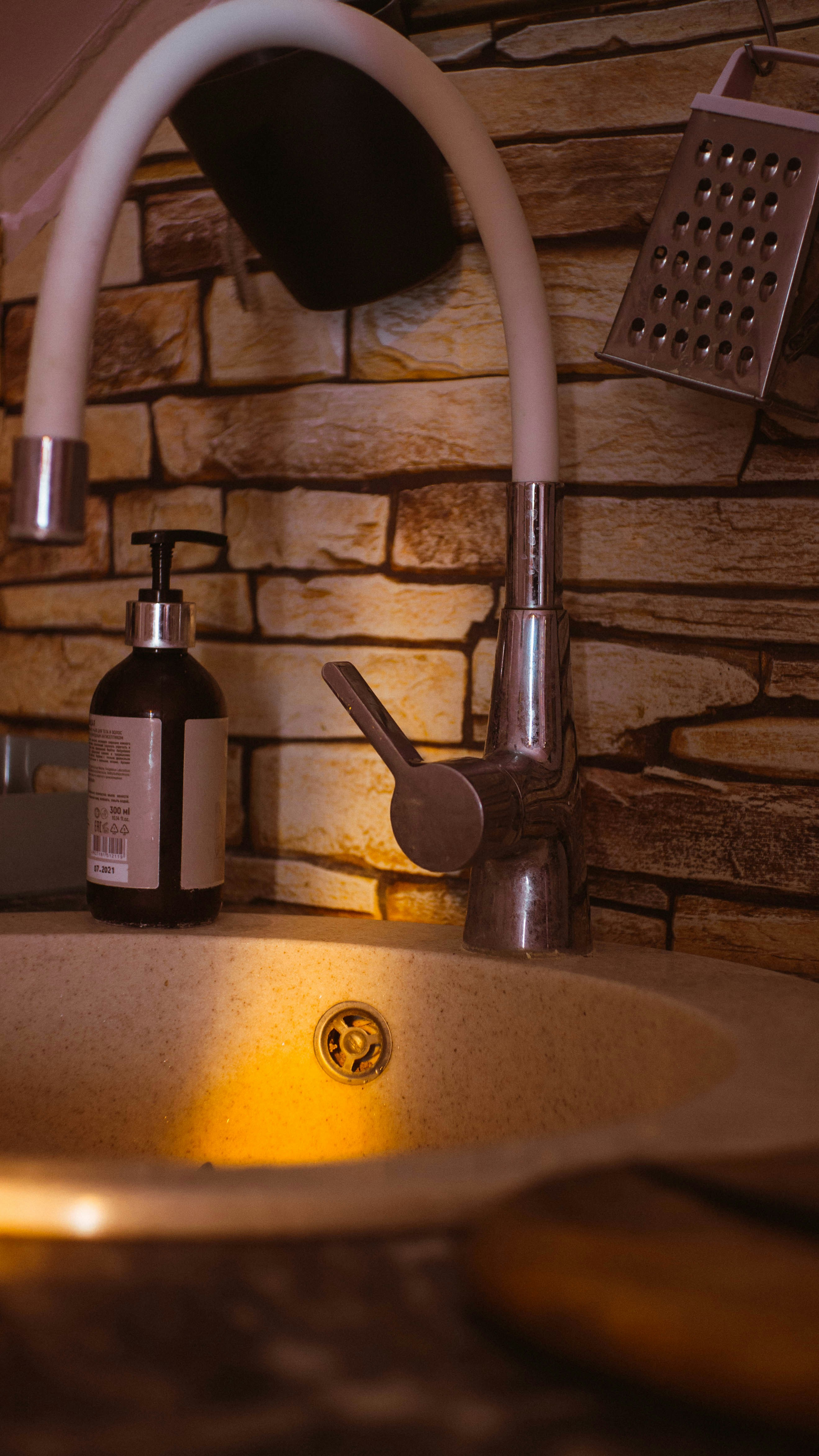 Amber Arc Over the Sink: A Close-Up of a Curved Faucet in Warm Brick Kitchen Light