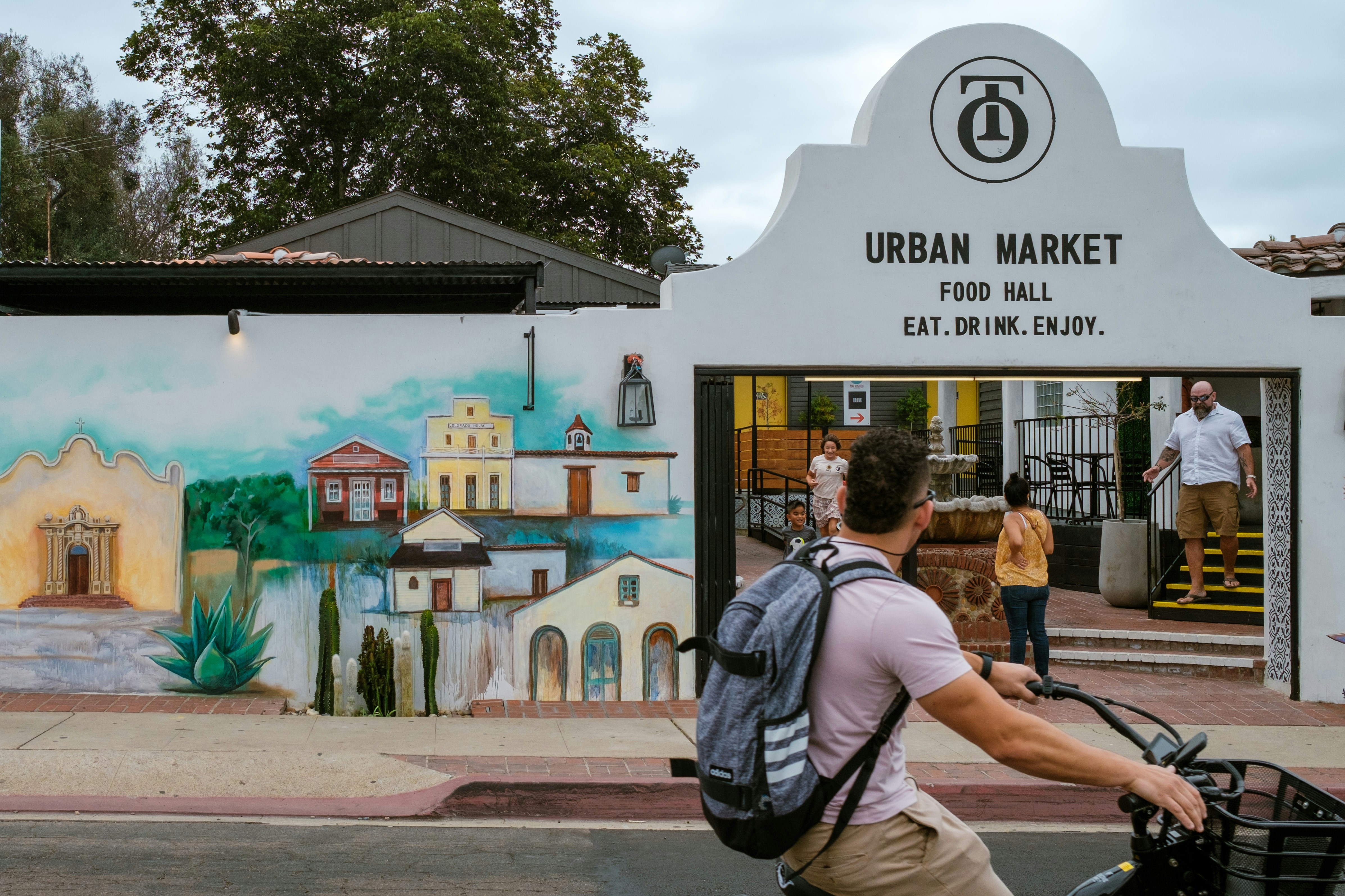Cyclist Navigates a Colorful Market Arch Framed by a Mural